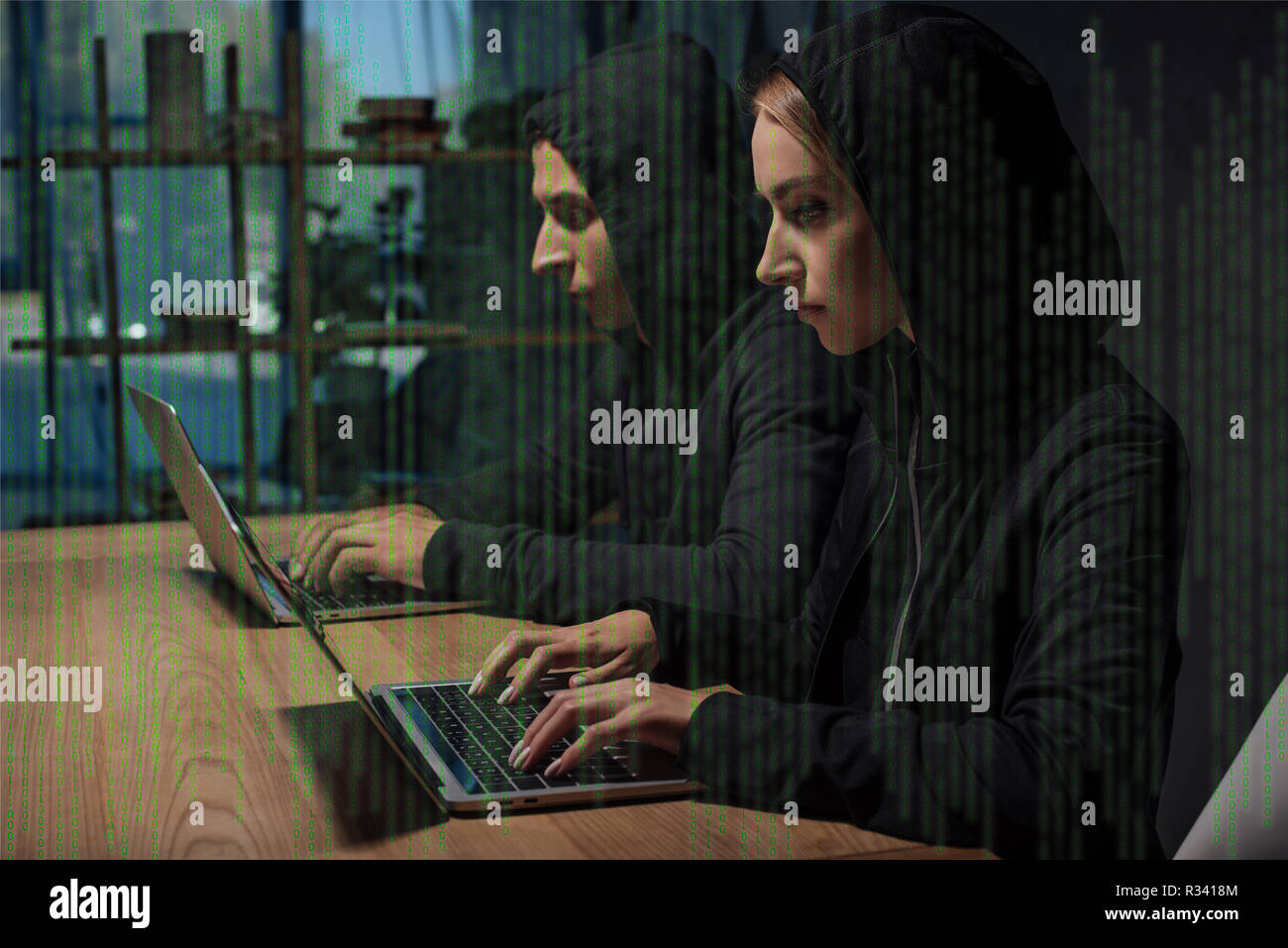 side view of hackers in black hoodies using laptops at wooden tabletop ...
