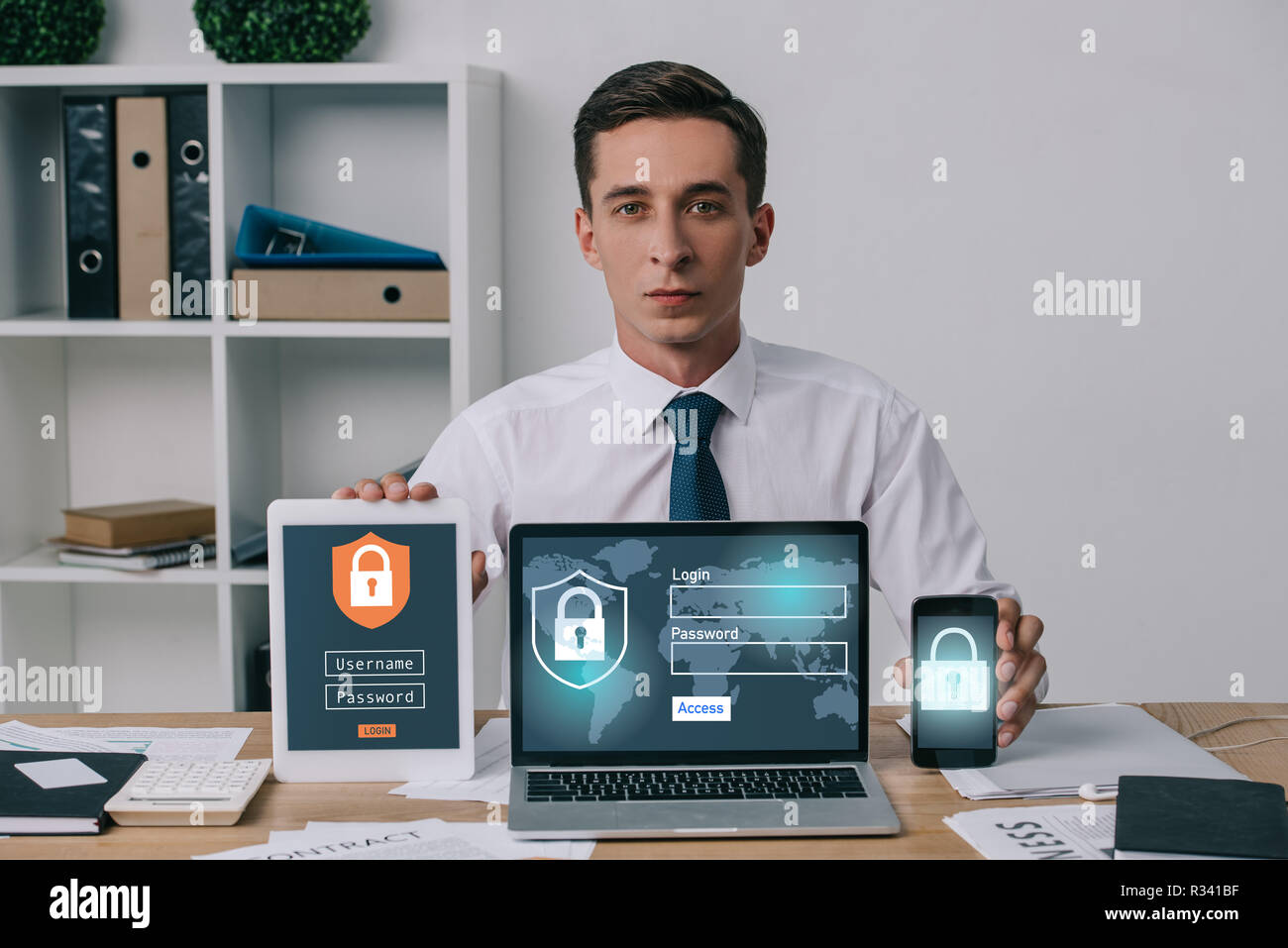 portrait of businessman showing laptop, tablet and smartphone with ...