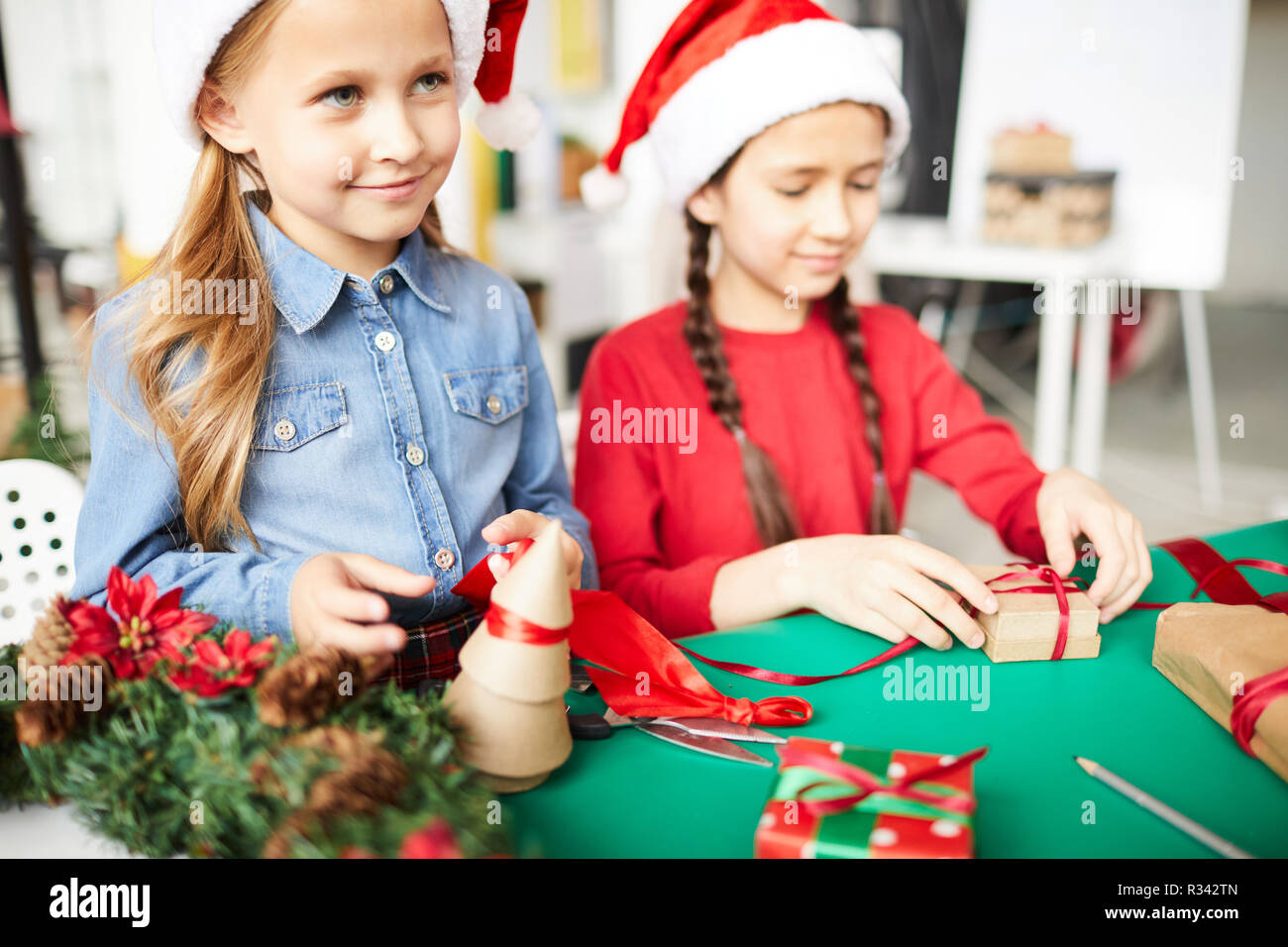 Cute little girl tying silk red ribbon aroung wooden firtree with her ...