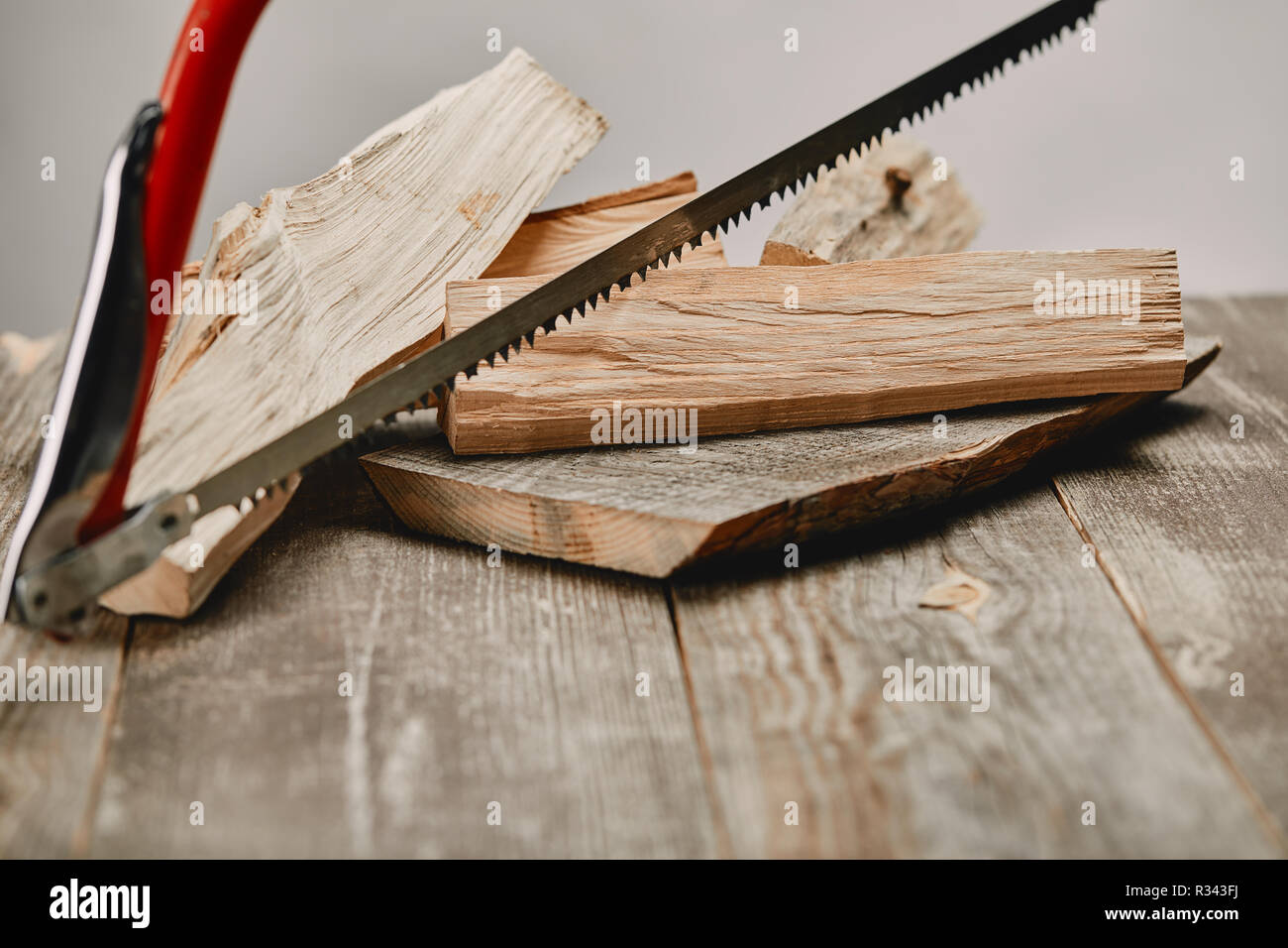 Close up view of hacksaw and wood logs on wooden table on grey ...