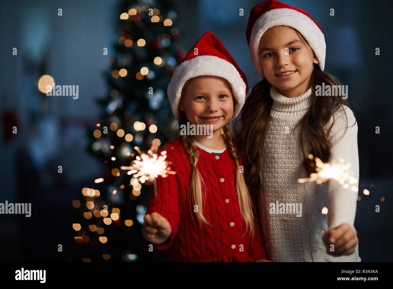 Happy little siblings in Santa caps holding sparkling bengal lights on ...