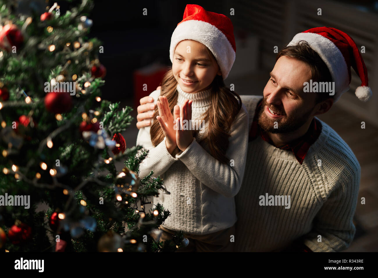 Cute little girl admiring Christmas tree after decorating it with ...