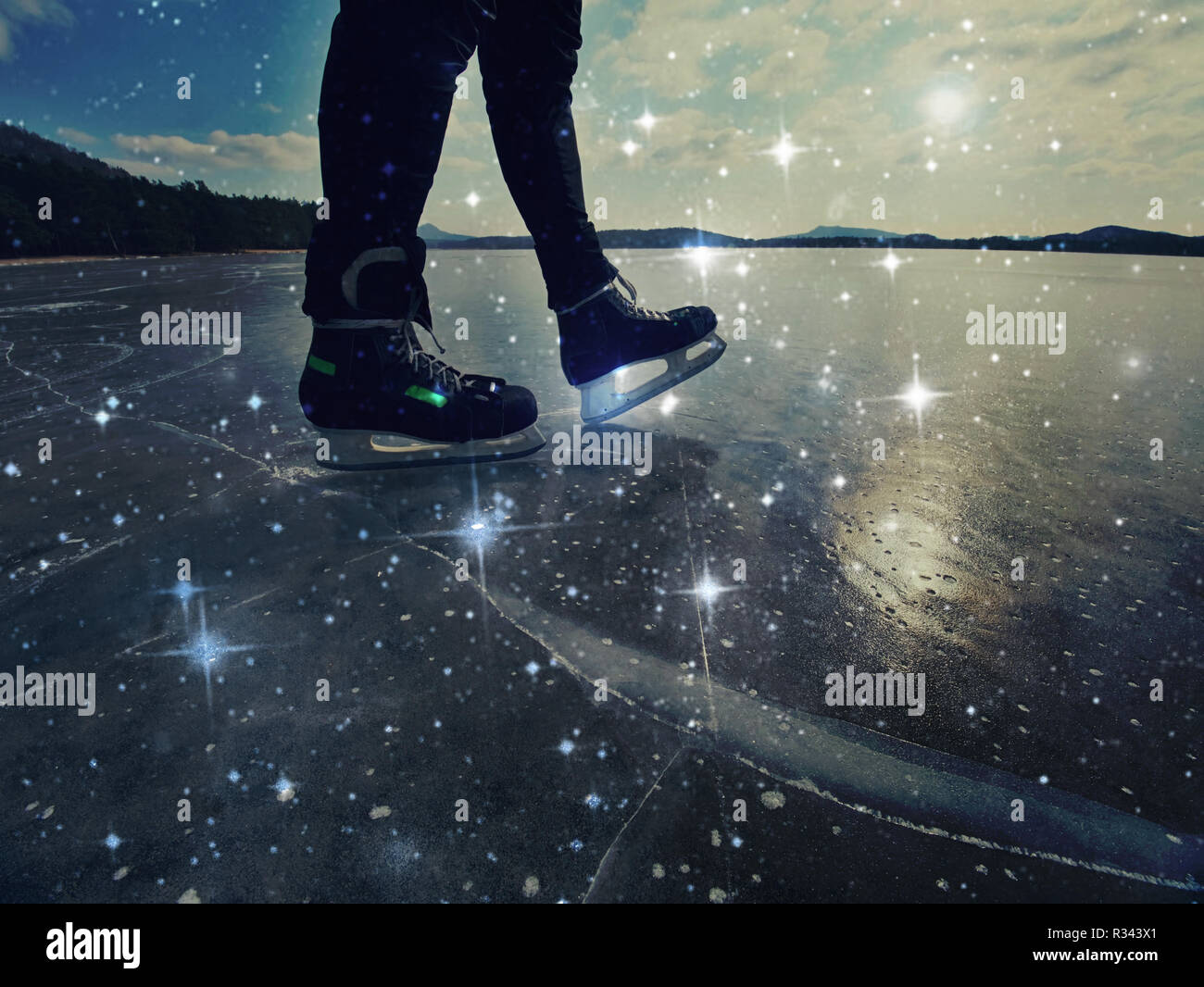 Man ice skating on frozen lake. Thin ice with deep cracks below man ...