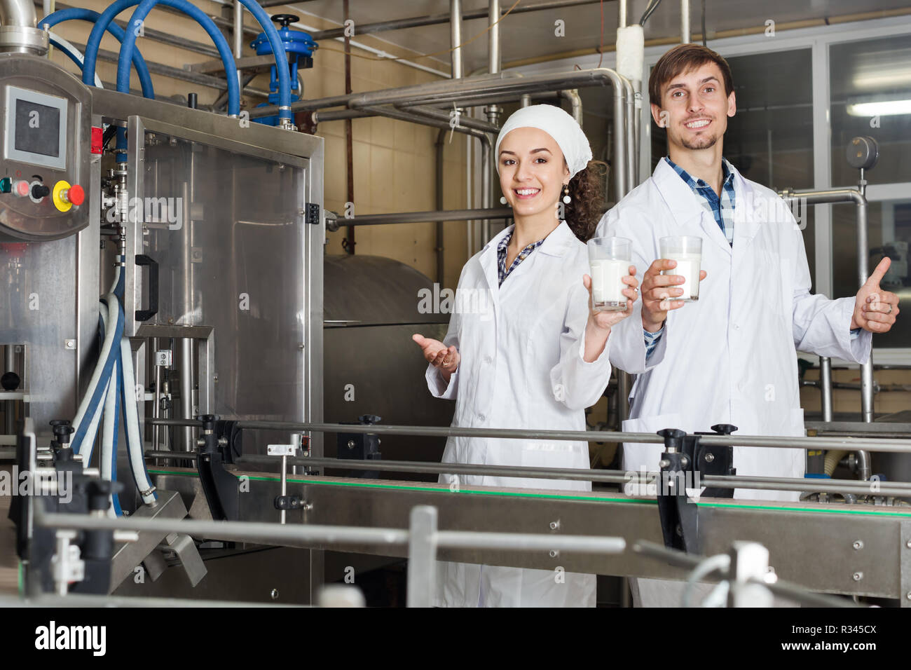 Two smiling workers in the lab coats showing their dairy production ...