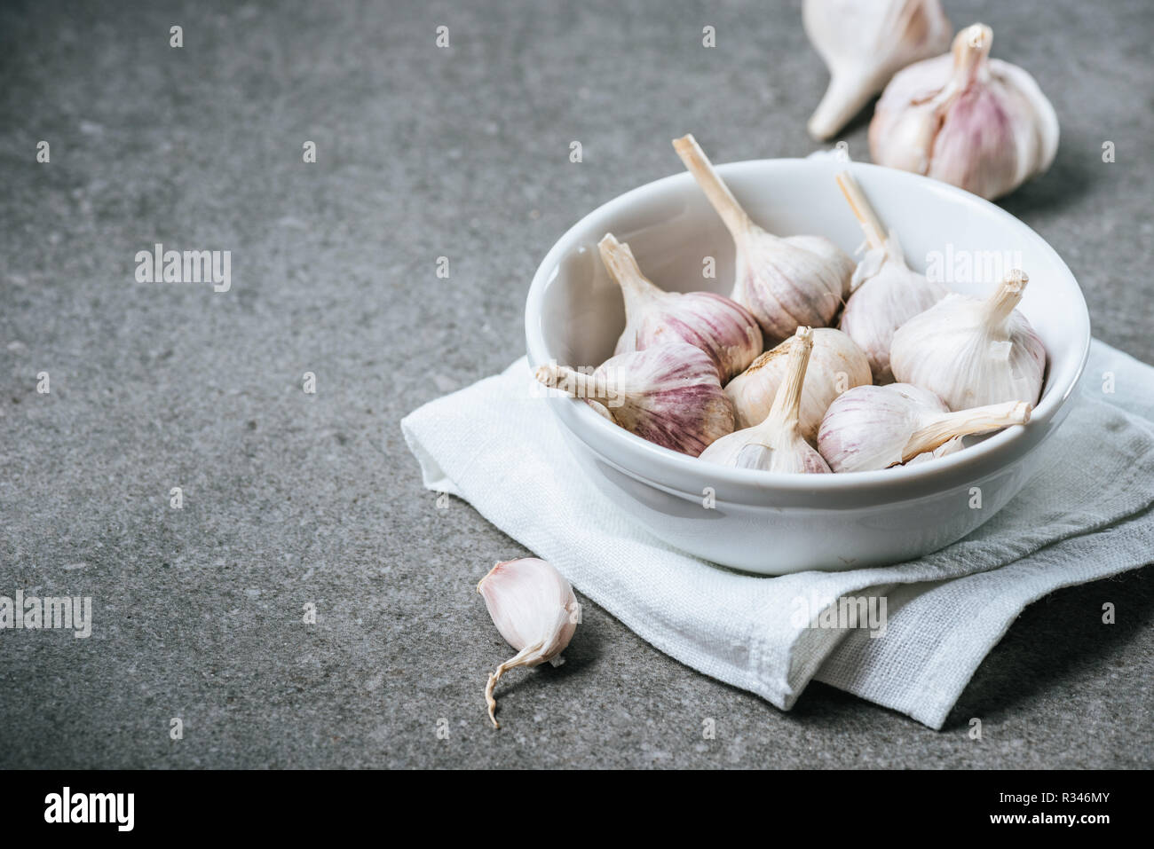 Ripe garlic heads in ceramic bowl on white napkin and peeled clove on ...