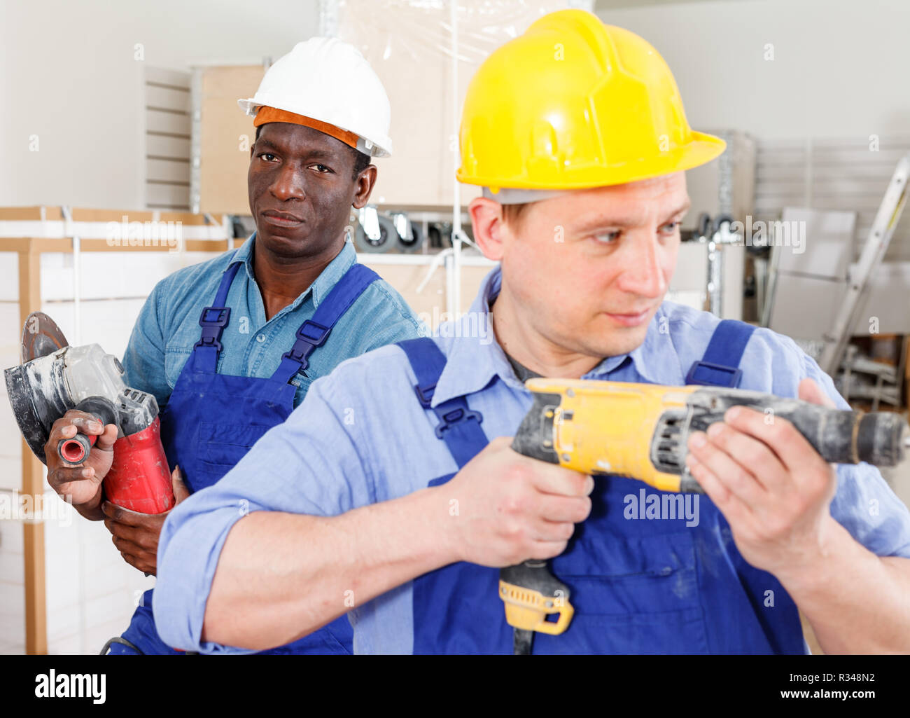 Two male builders working with electric tools at indoors building site ...