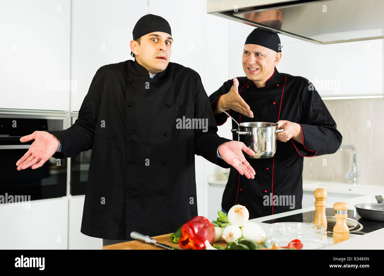 Two men cooks in black uniform discussion and having quarrel on kitchen ...