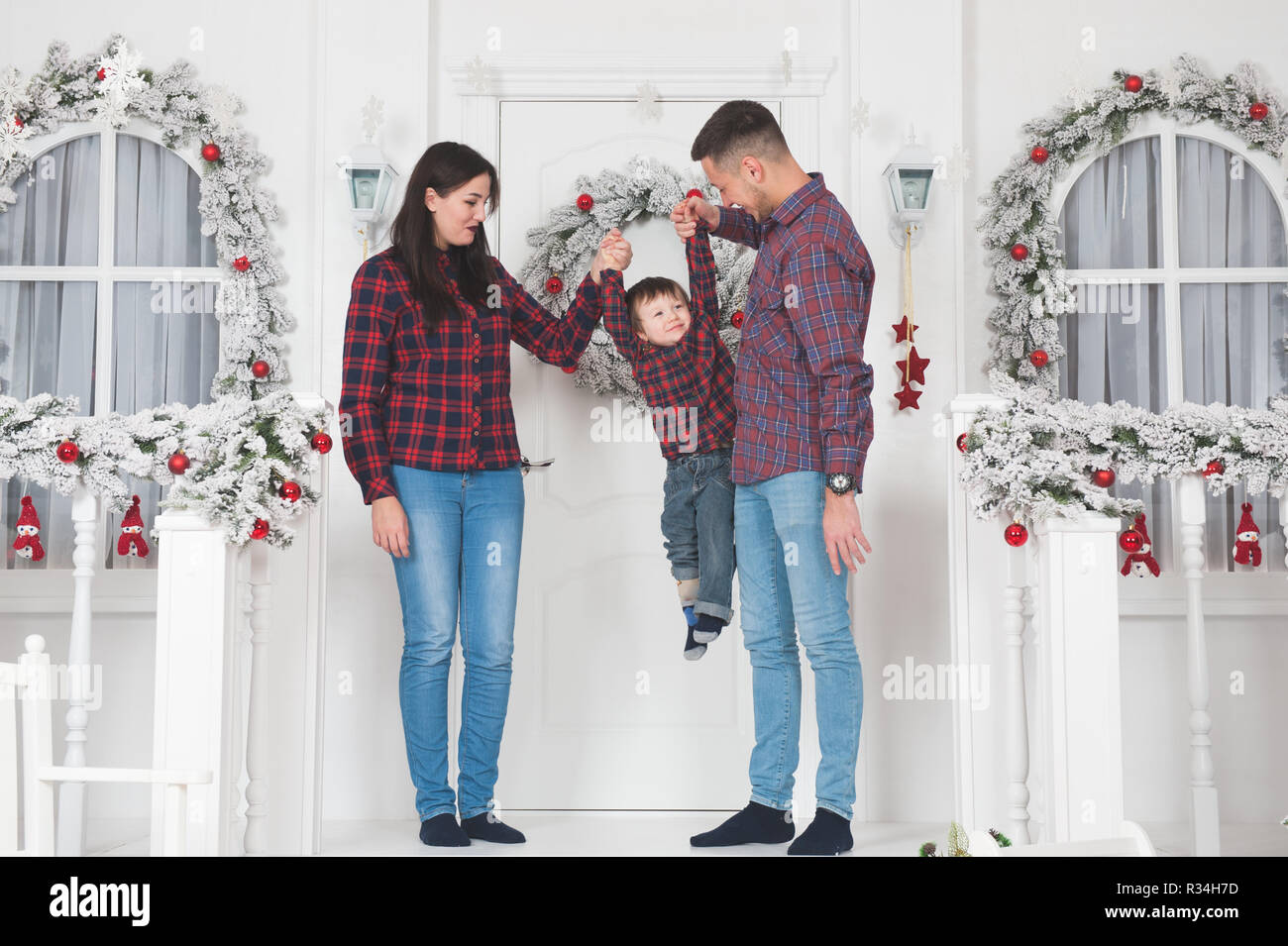 young mother and father raising child up on porch of christmas house ...