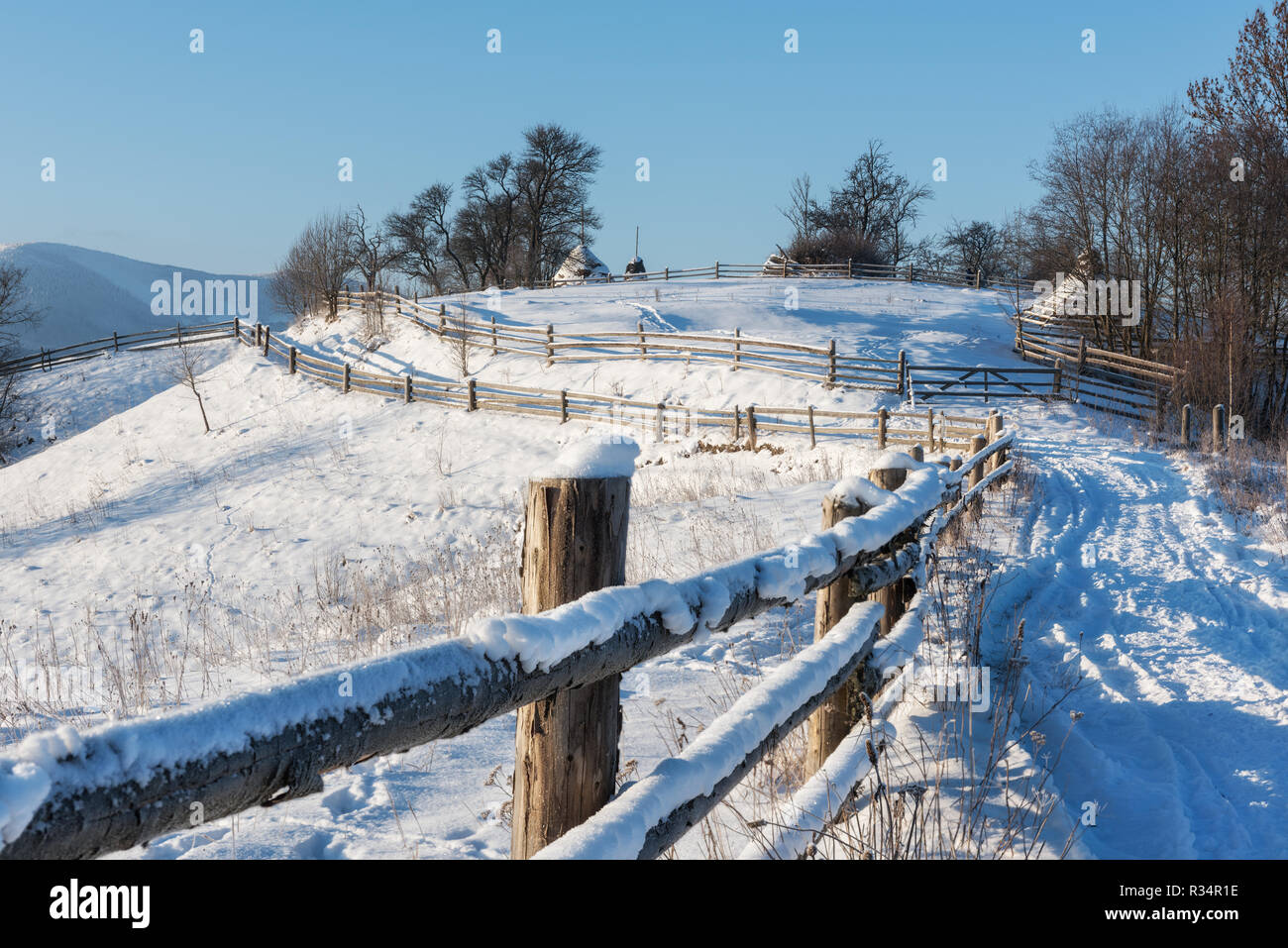 Rural alpine winter landscape with fence and path, serene blue sky ...