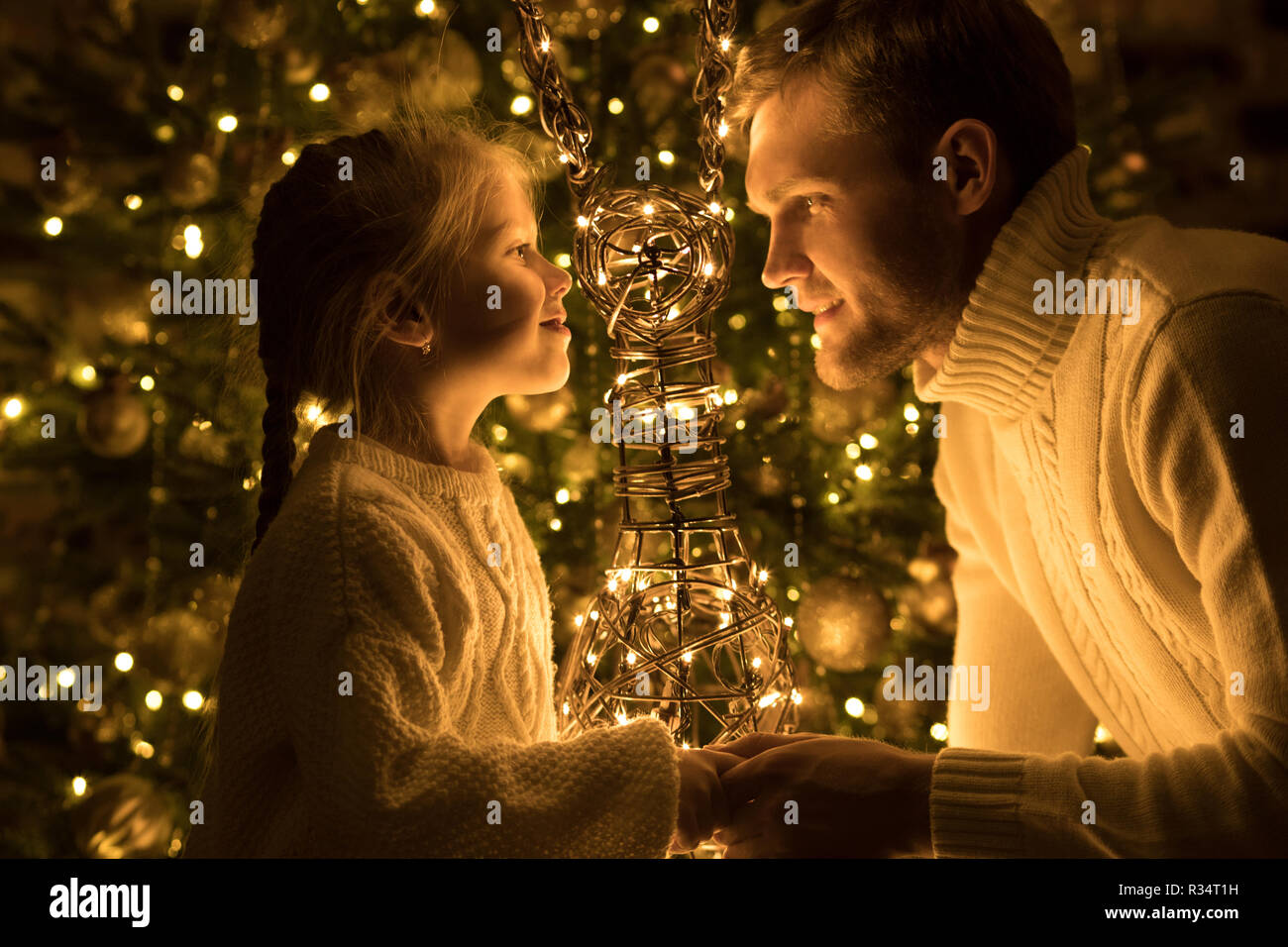 Father and daughter sit near the Christmas tree with decorative deer ...
