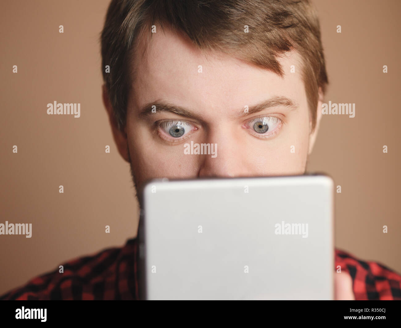 Young emotional man, looking down at pda on beige background Stock ...