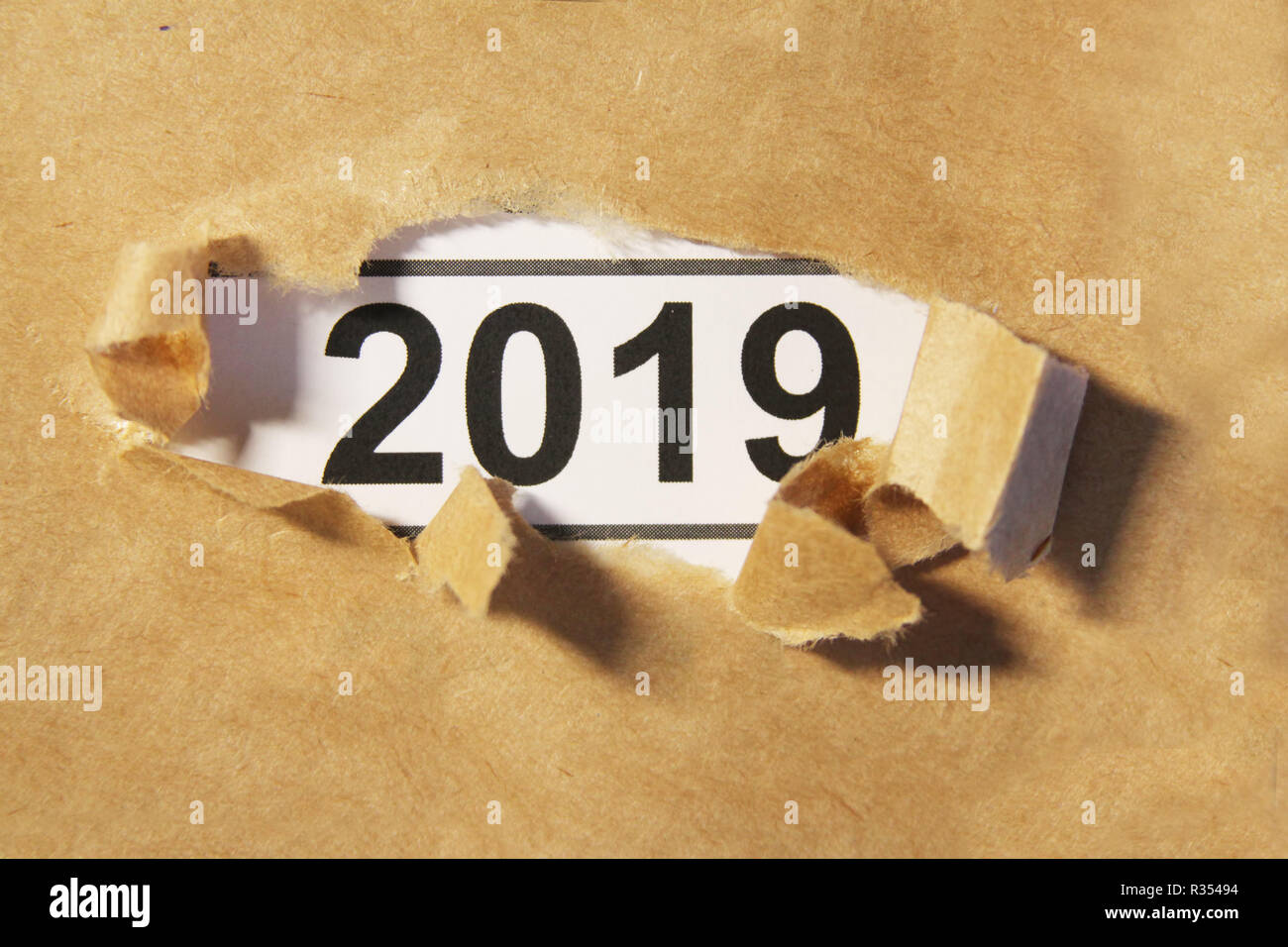 2019 appearing behind ripped brown paper Stock Photo - Alamy