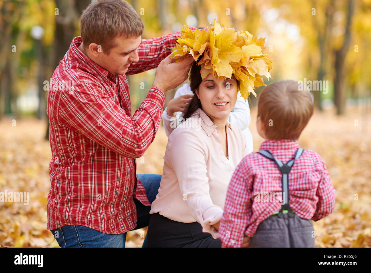 Father and son put yellow fallen leaves on mother head. Happy family is ...
