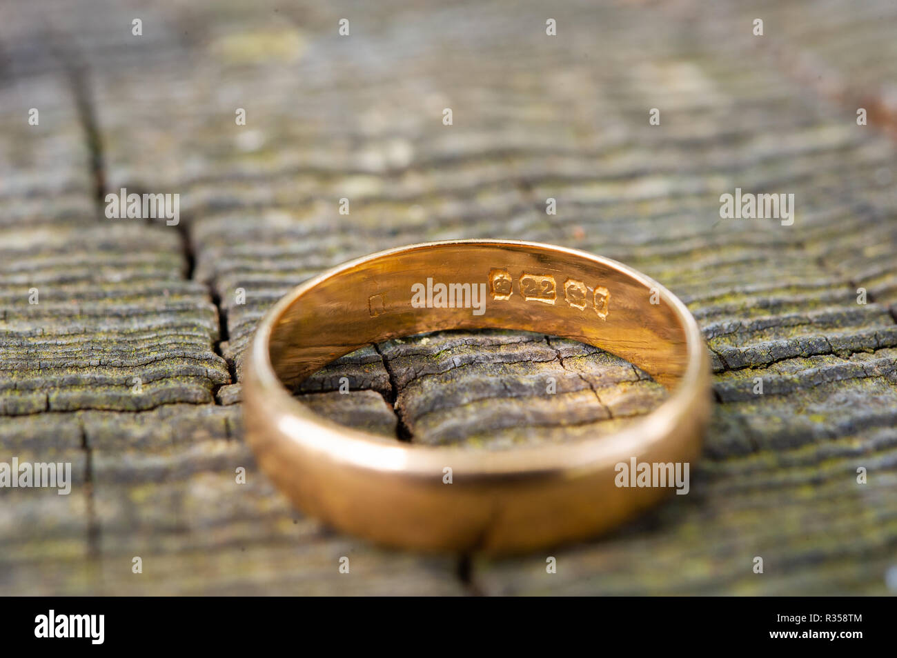 A 22ct gold wedding ring against a background of old textured wood with ...