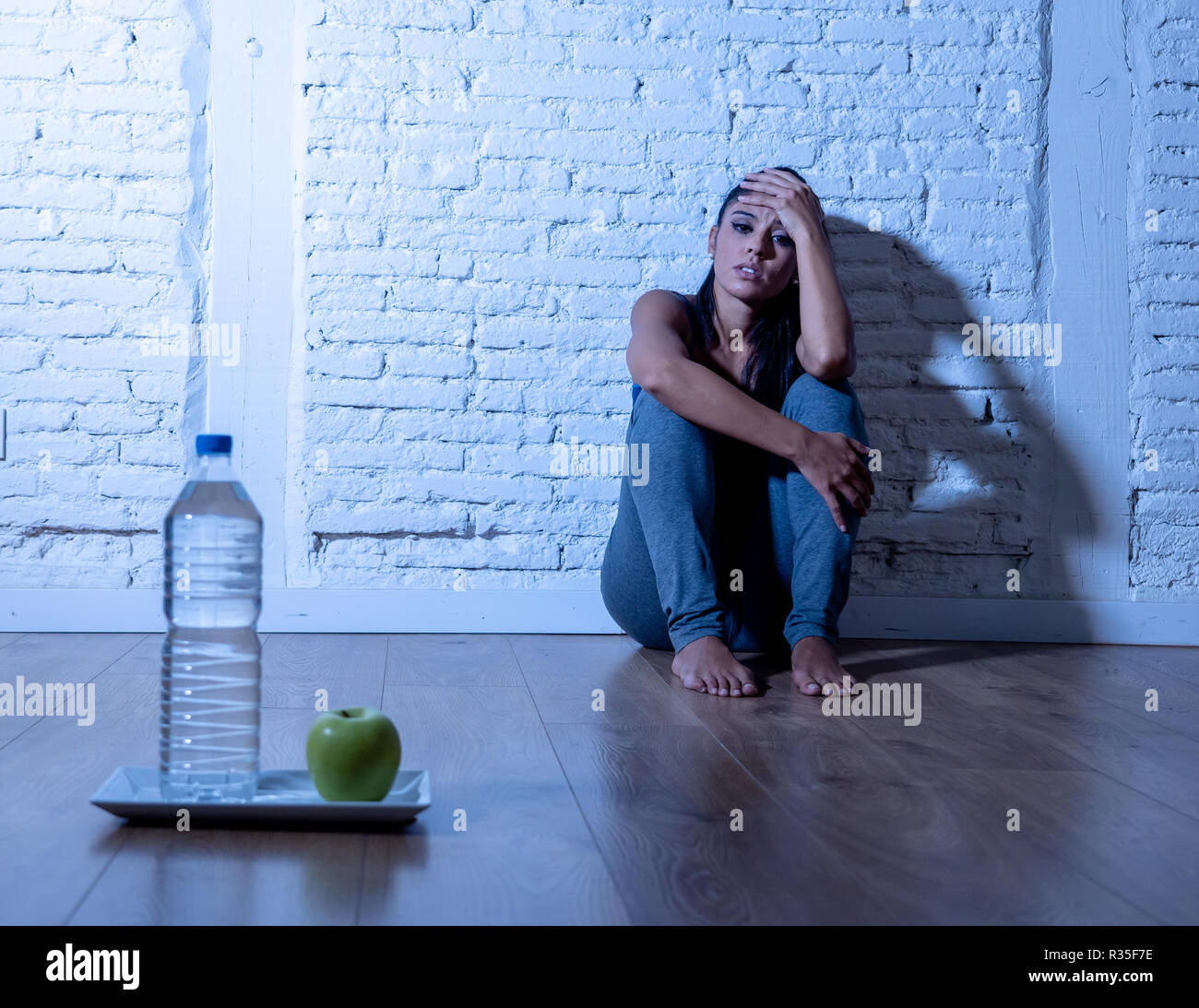 Desperate dieting young woman sitting on the ground looking sad at one ...