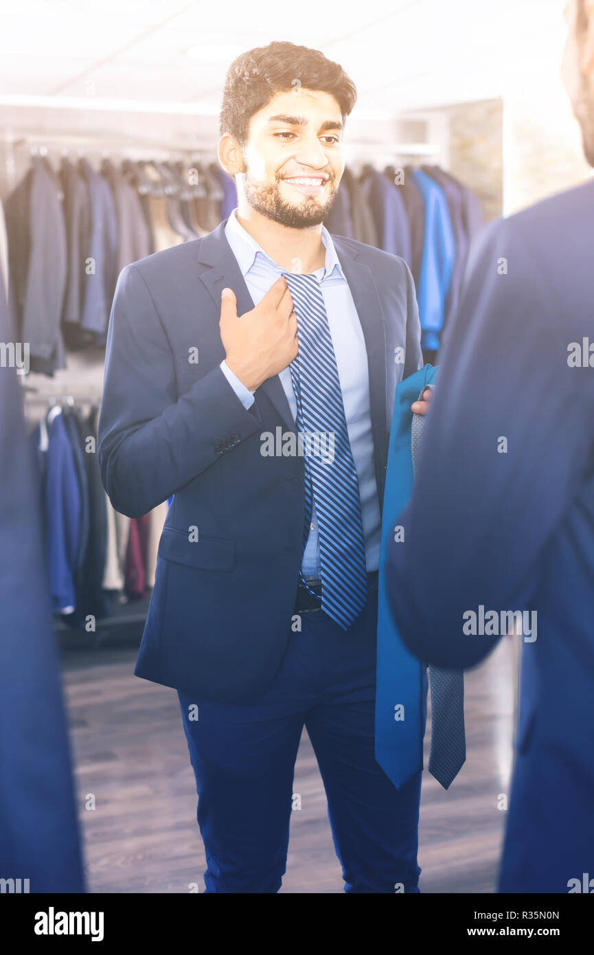 Customer male is picking up tie for jacket in front of the mirror in ...