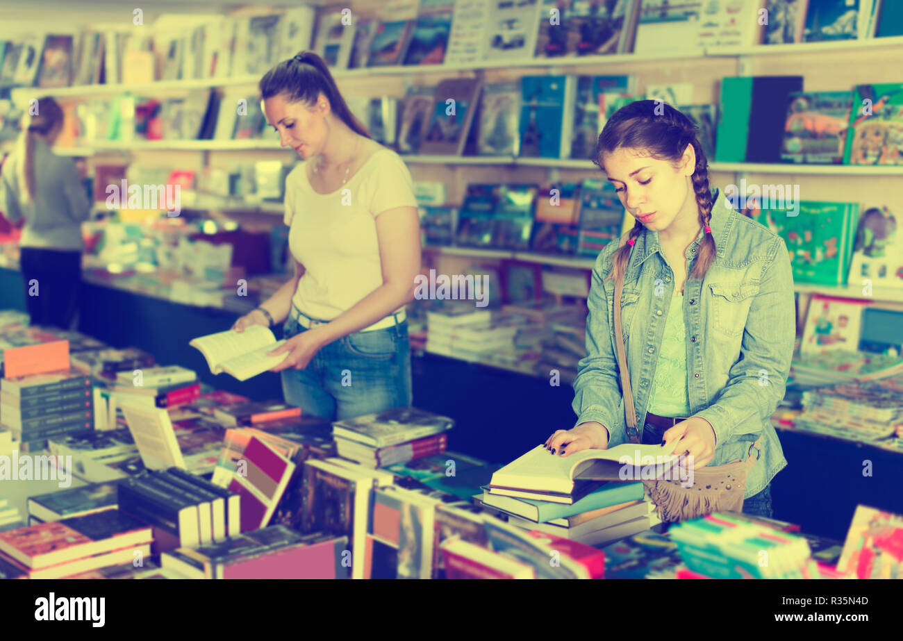 glad woman showing open book to thoughtful girl in school age in book ...