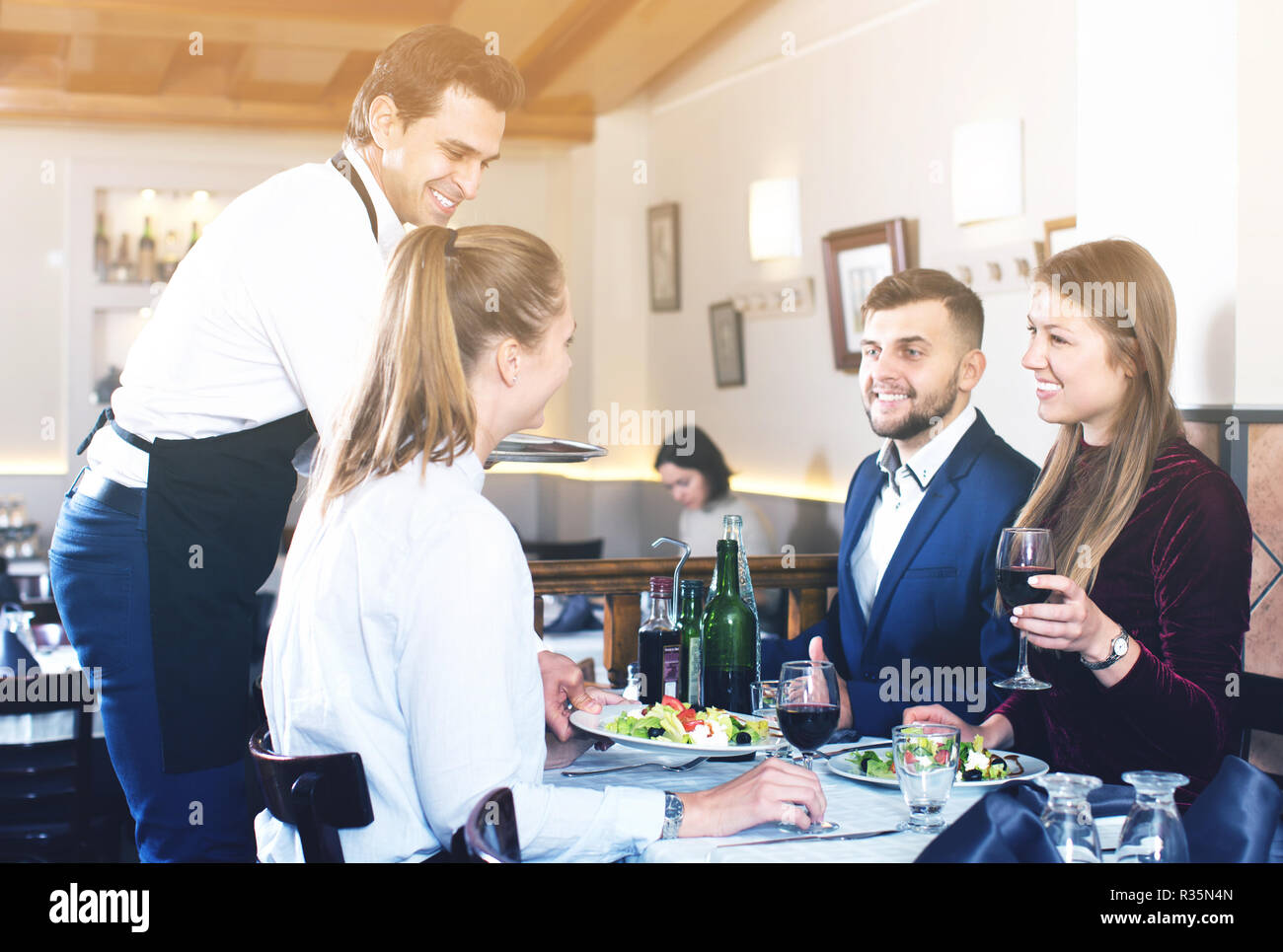 Handsome waiter serving meals to friendly company guests at restaurant ...