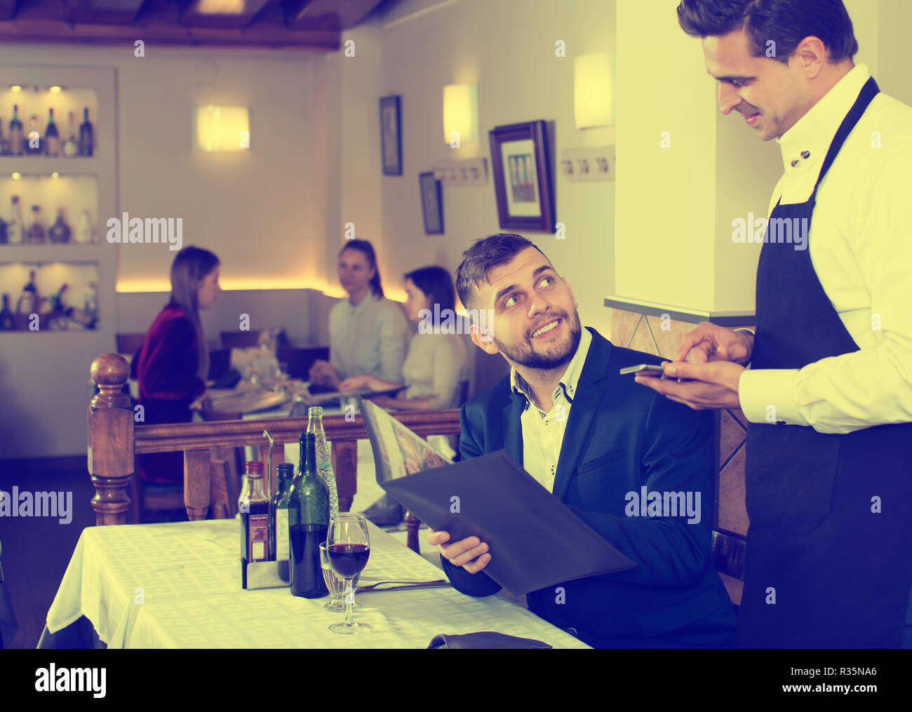 Positive waiter taking order in restaurant, helping young male with ...