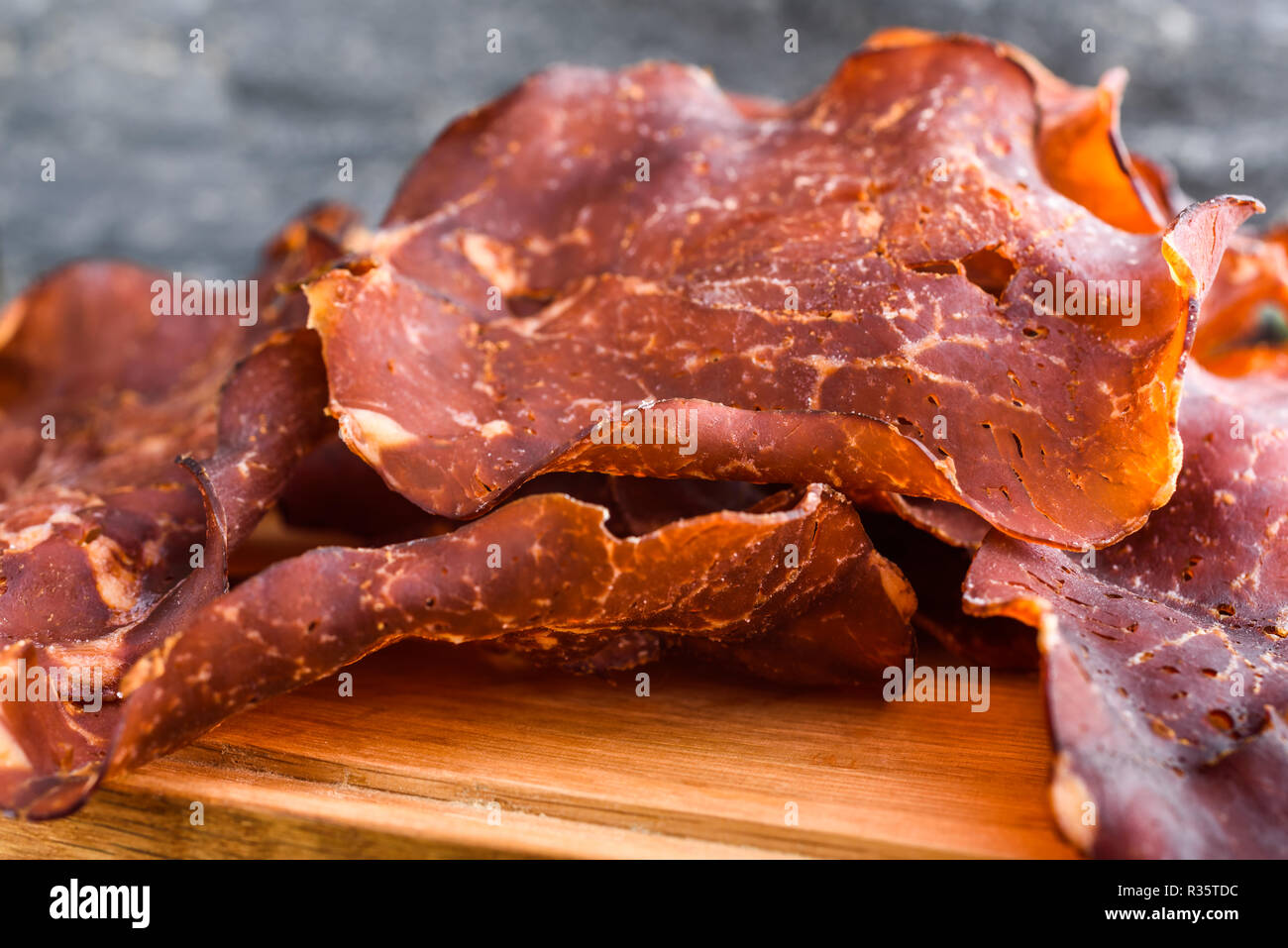 Thinly sliced and dried smoked ham on oak tray. Small crystals of salt ...