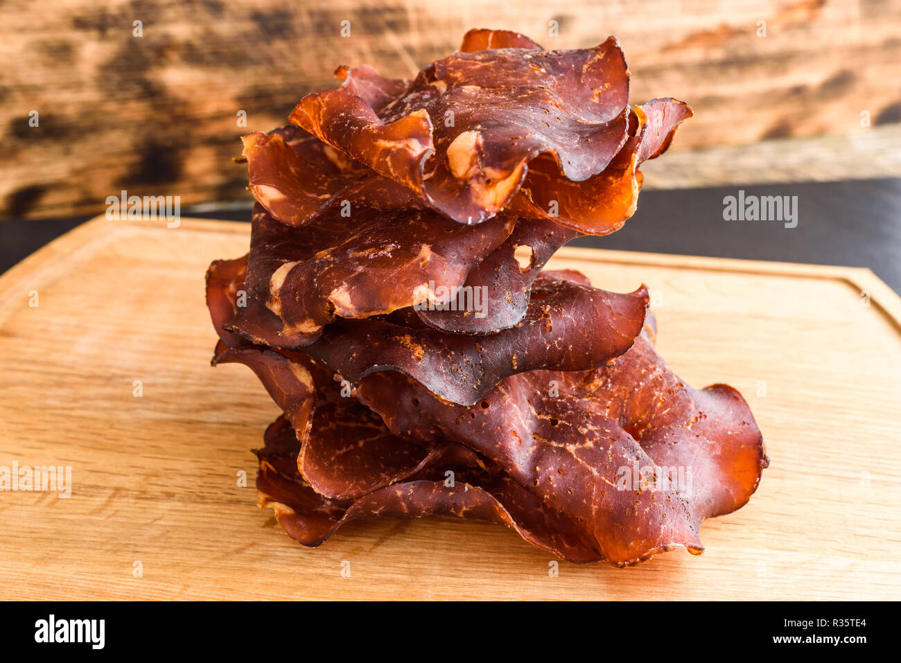 Thinly sliced and dried smoked ham on oak tray. Small crystals of salt ...