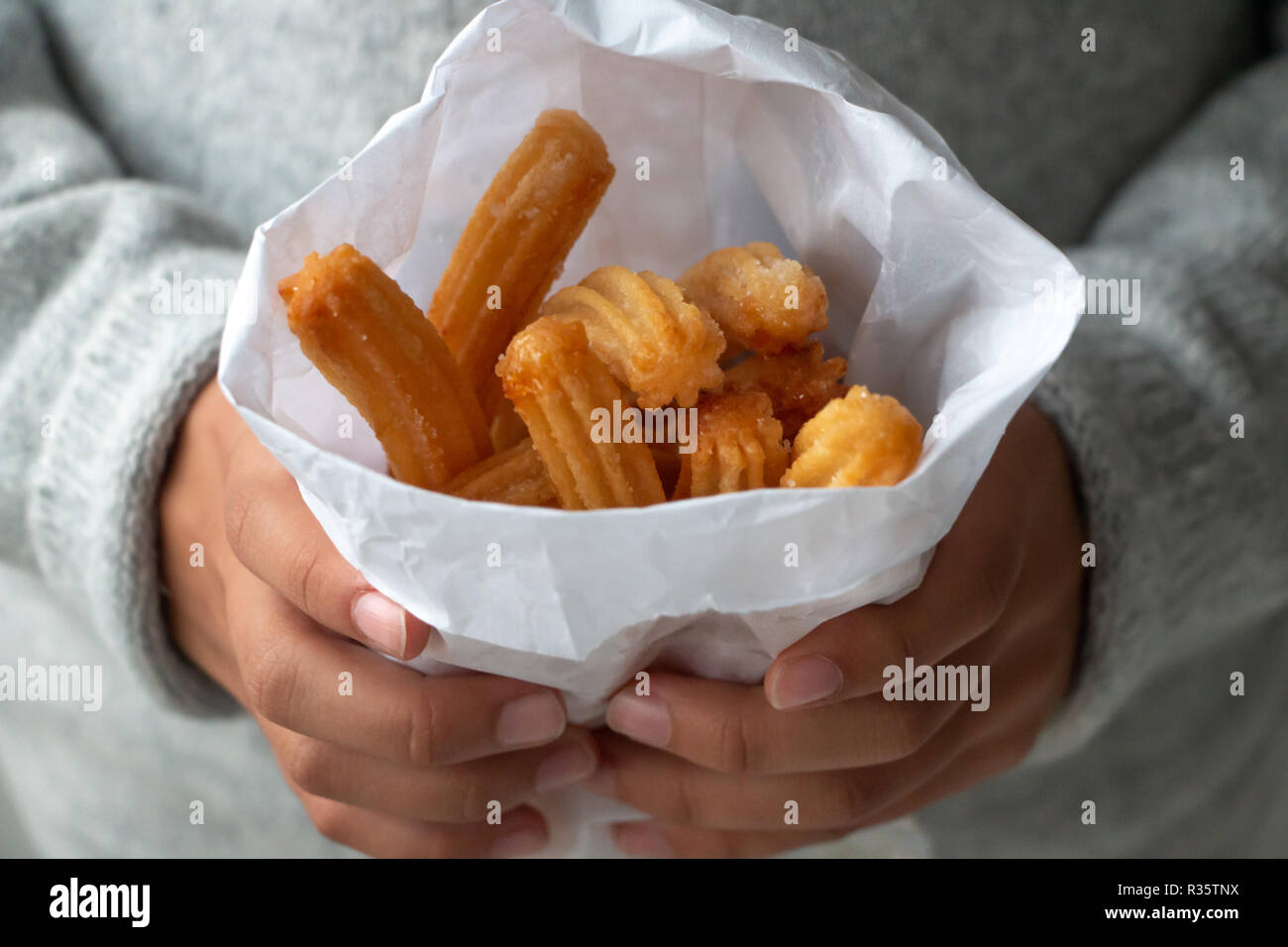 Little girl hands holding churros in a paper bag Stock Photo - Alamy