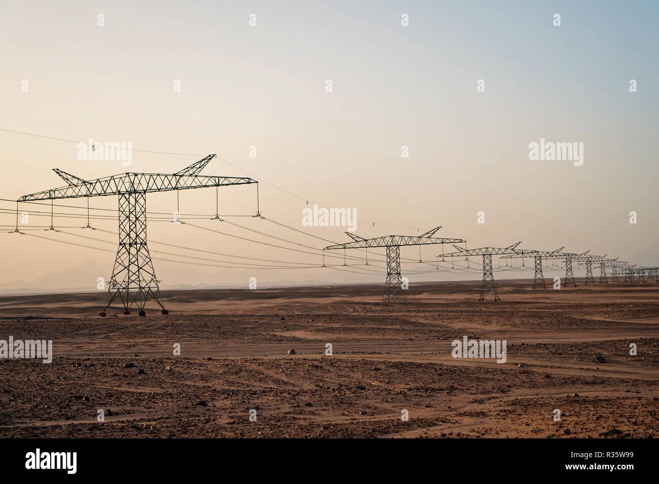 Electricity pylons and high voltage power lines in sand desert land ...