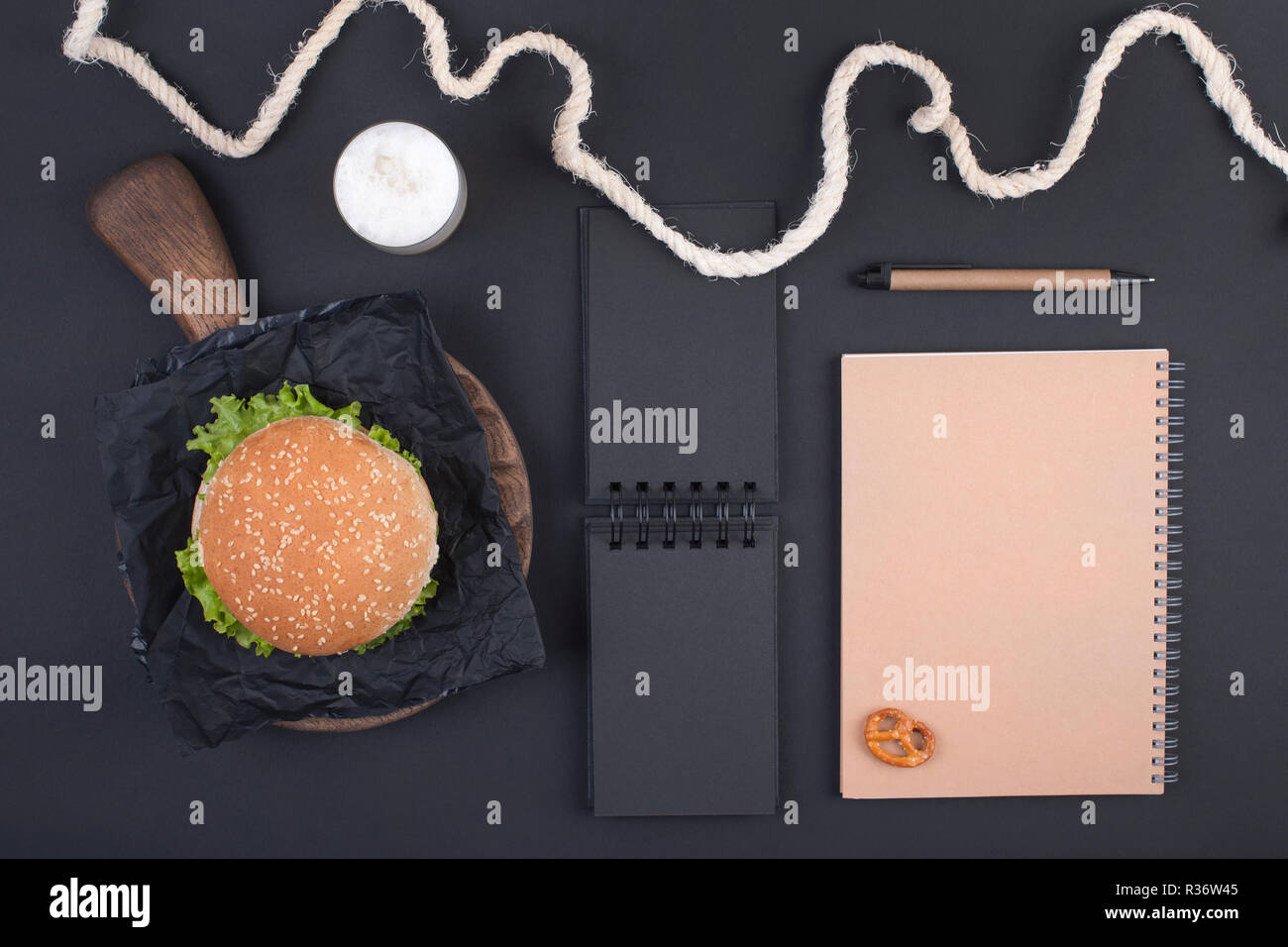 Big hamburger, beer and notebook for planning on a black background ...