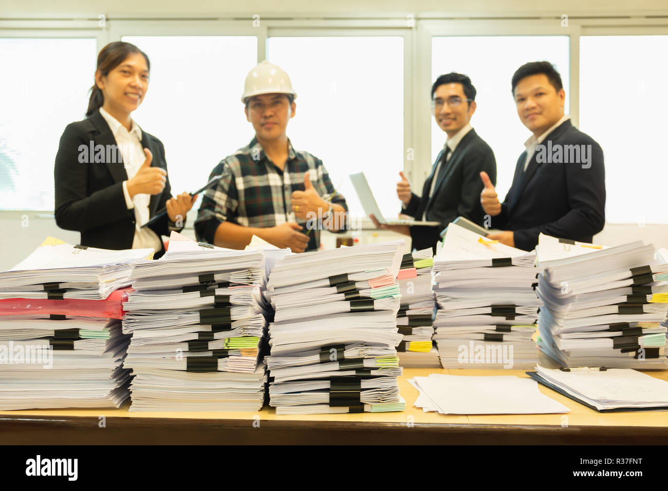 Pile of paperwork on table with group of happy business people standing ...