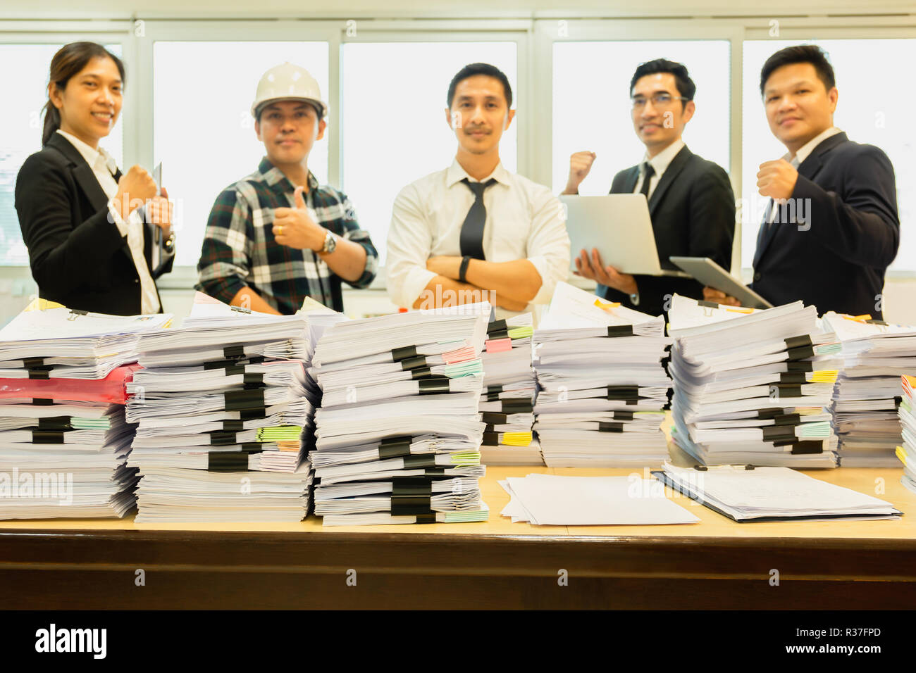 Pile of paperwork on table with group of business people giving hand up ...