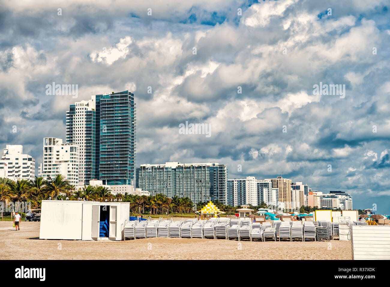 sunbeds stacked on sand beach, green palm trees and high rise ...