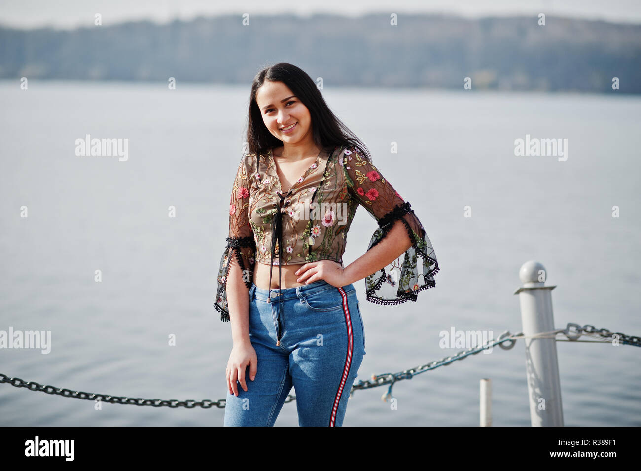 Pretty latino model girl from Ecuador wear on jeans posed against lake ...