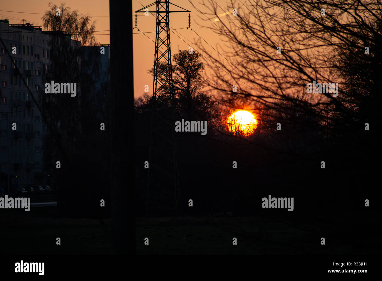 red sunset with sun setting down behind large electricity power line ...