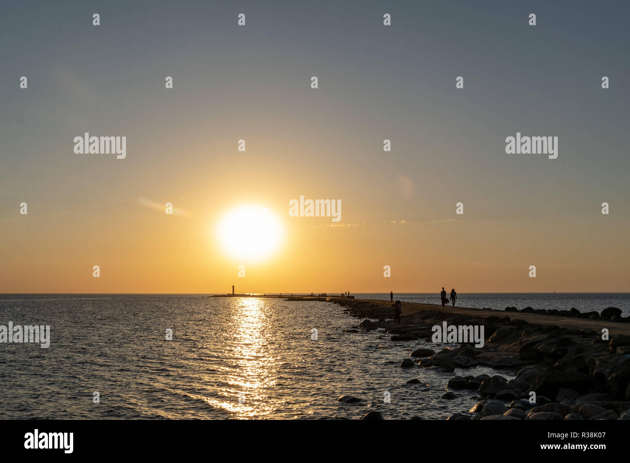 breakwater in the sea with red lighthouse at the end at the sunset with ...