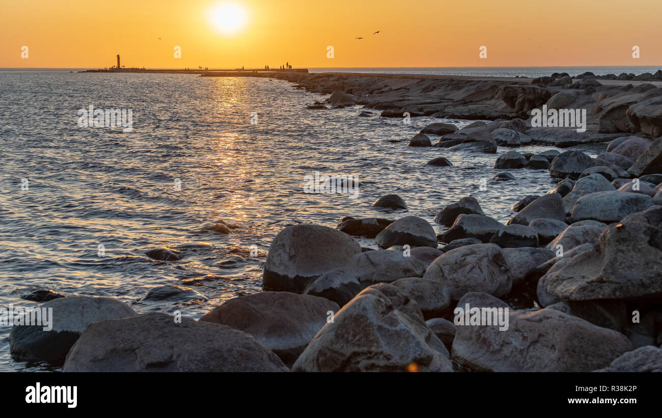 breakwater in the sea with red lighthouse at the end at the sunset with ...