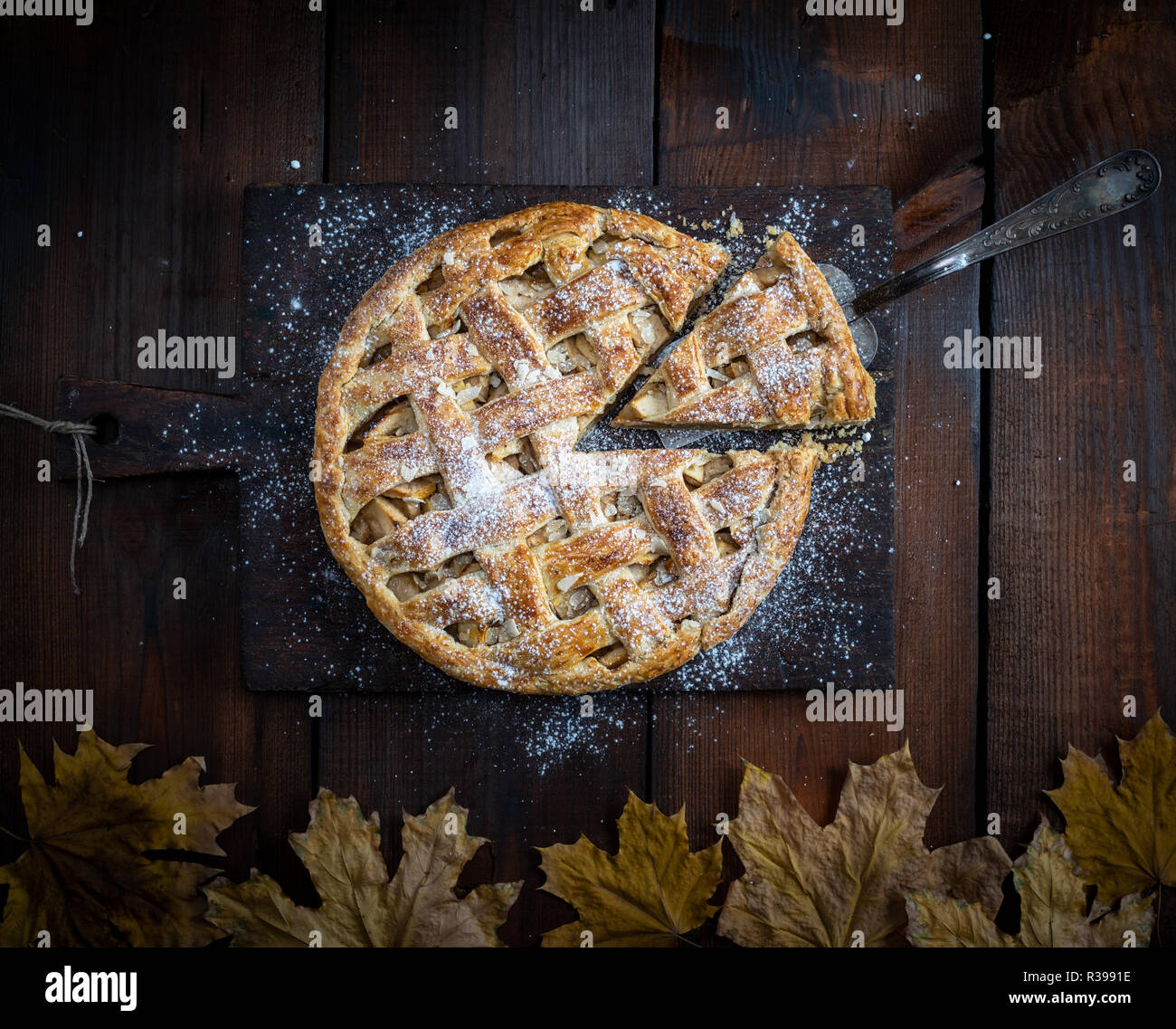 baked whole round apple pie on a rectangular old brown cutting board ...