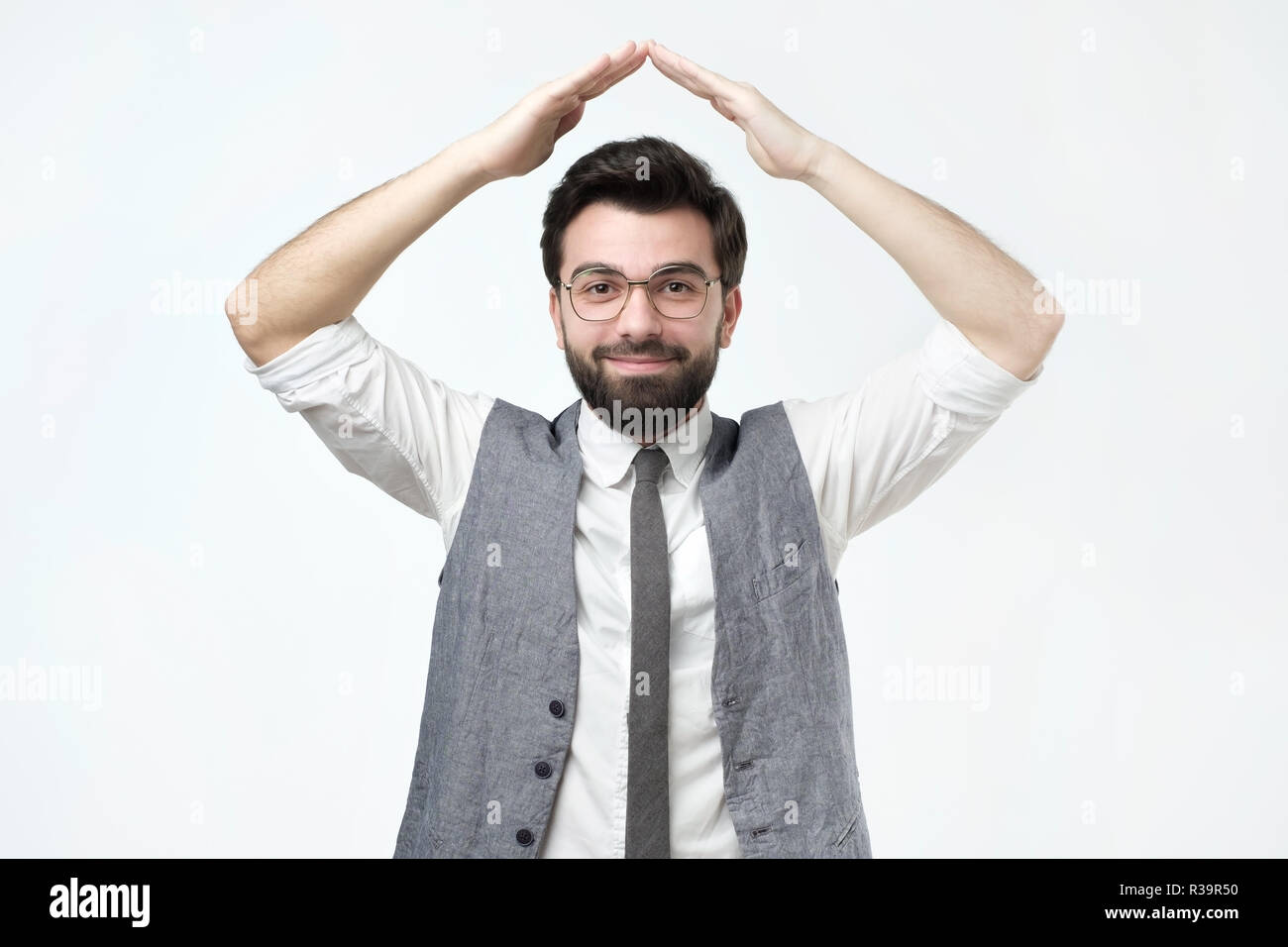 Cheerful man holding hands over head like a roof house on gray ...