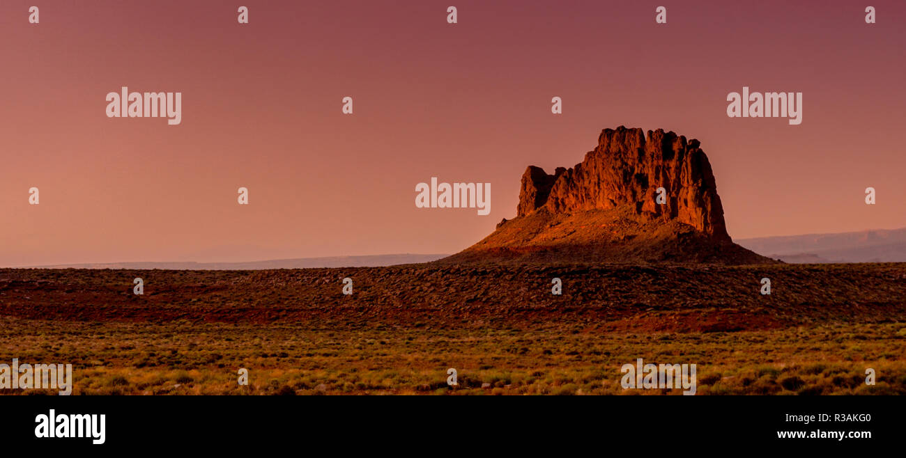 colorful desert sunset over a single rock butte or mesa rock formation ...