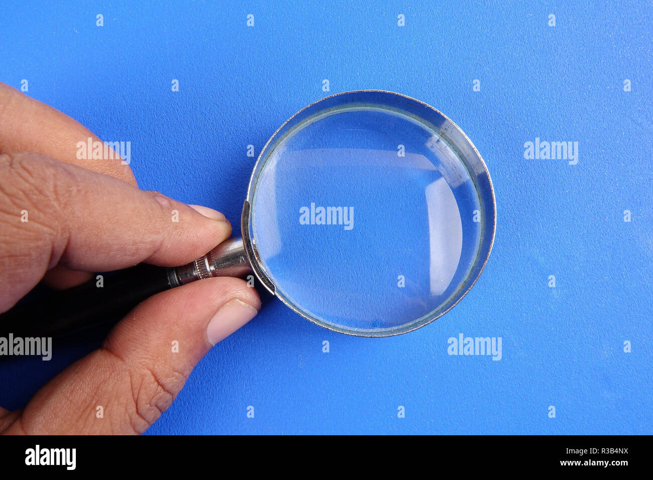 Hand holding magnify glass over a blue background Stock Photo - Alamy
