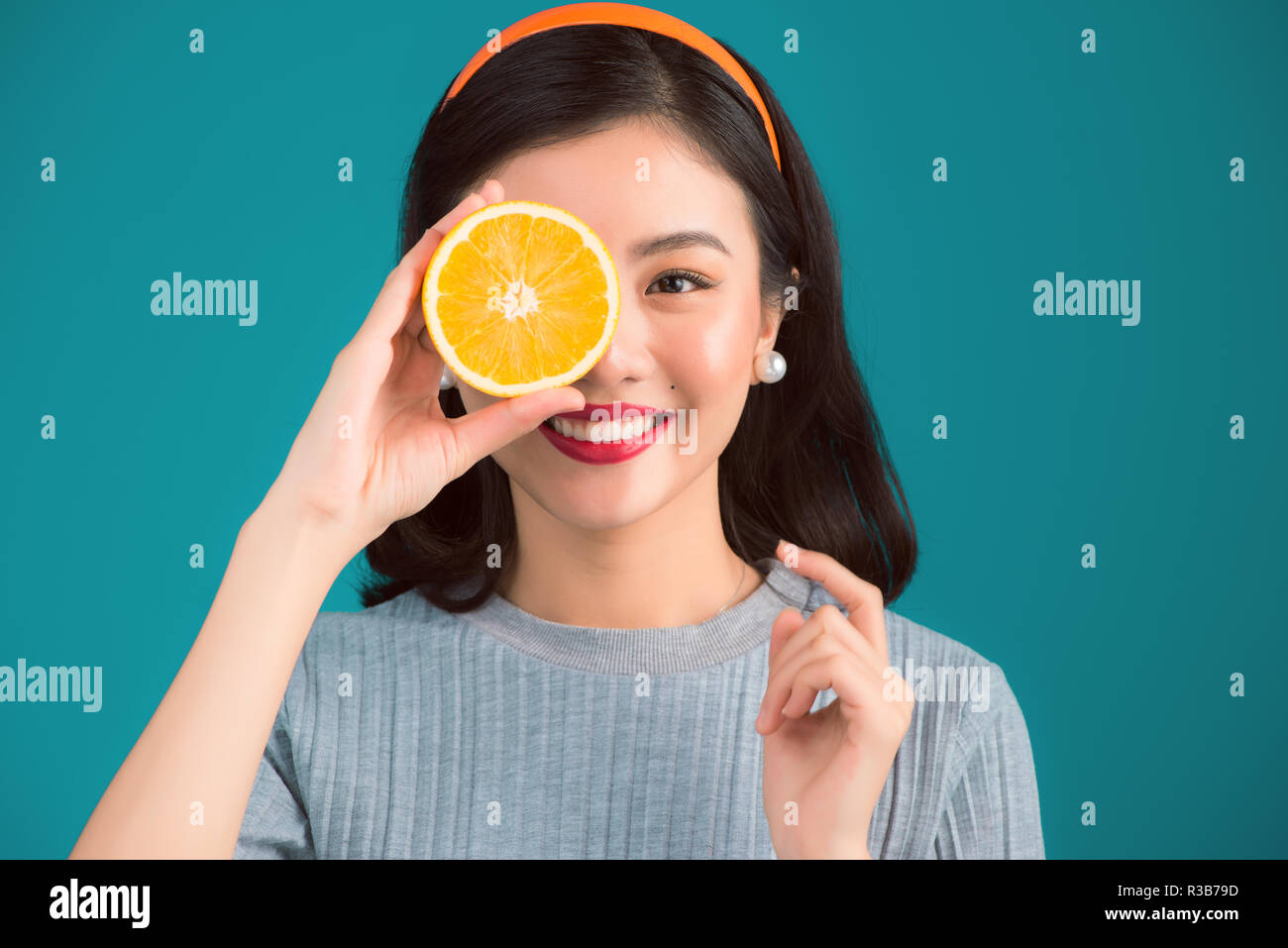 Healthy food. Smiling lovely pinup asian girl holding orange over blue ...