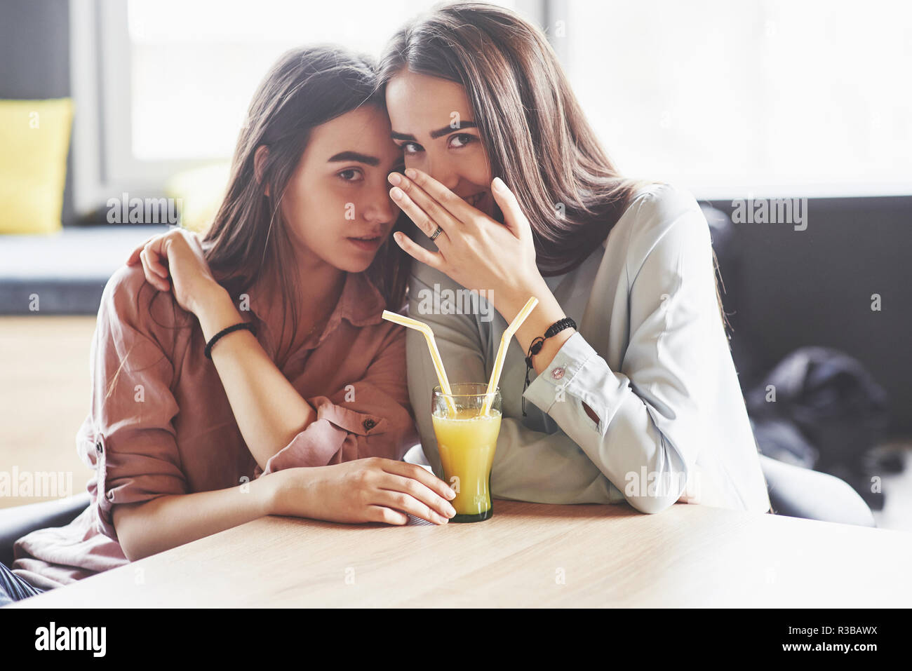 Two beautiful twin girls spend time drinking juice. Sisters relaxing in ...