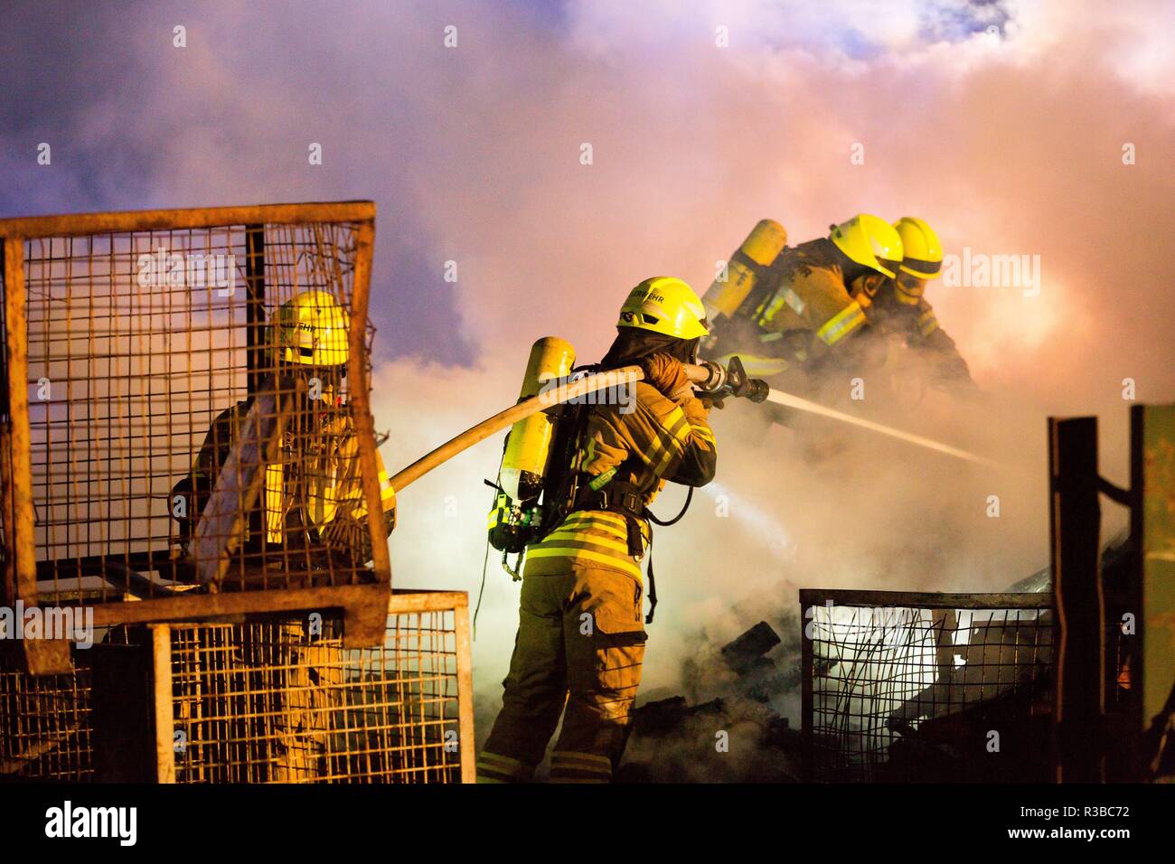 Firefighters with masks fighting a fire of a larger stock of firewood ...