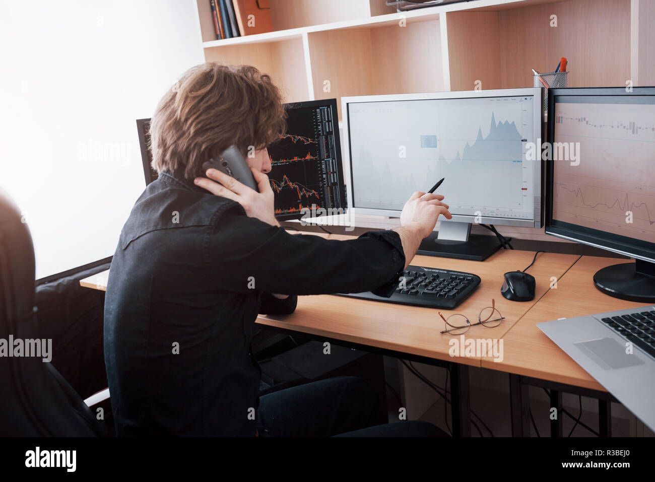 Over the shoulder view of and stock broker trading online while accepting orders by phone ...