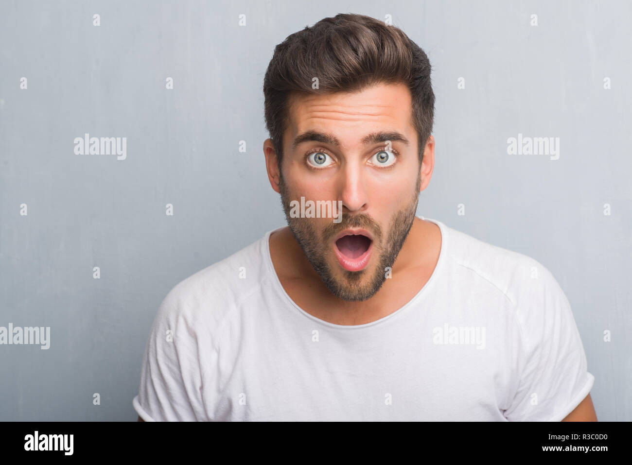 Handsome young man over grey grunge wall scared in shock with a ...