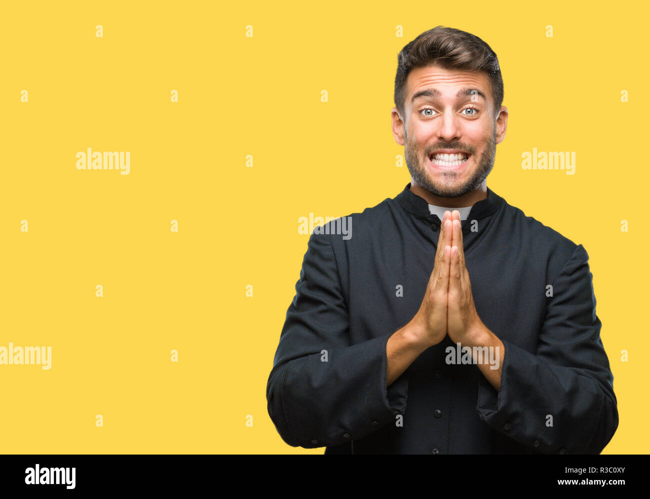Young catholic christian priest man over isolated background praying ...