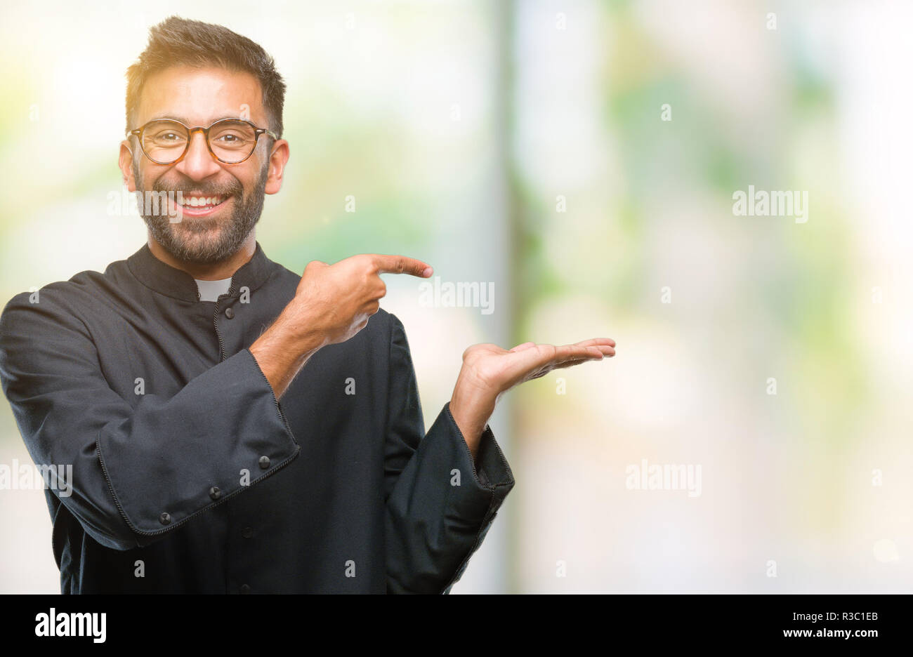 Adult hispanic catholic priest man over isolated background amazed and ...