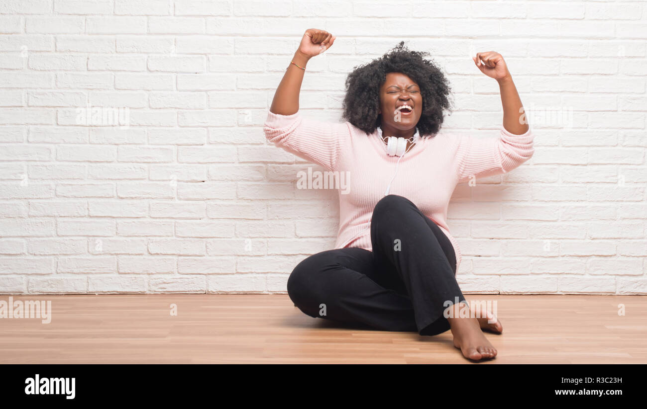 Young african american woman sitting on the floor wearing headphones ...