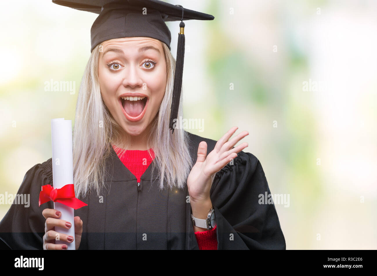 Young blonde woman wearing graduate uniform holding degree over ...