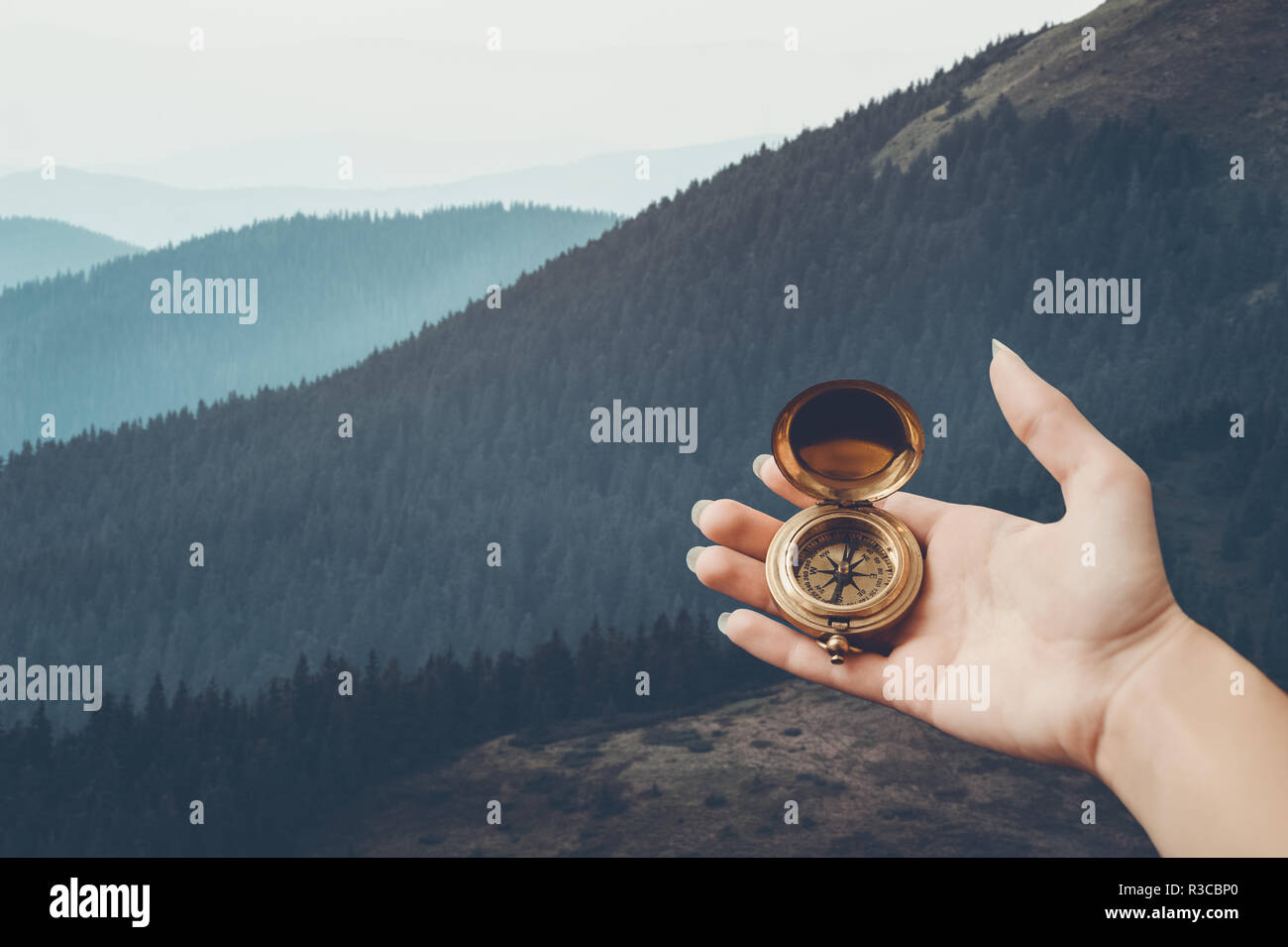 A hand holding vintage bronze compass. Blue gradient layered hills at ...