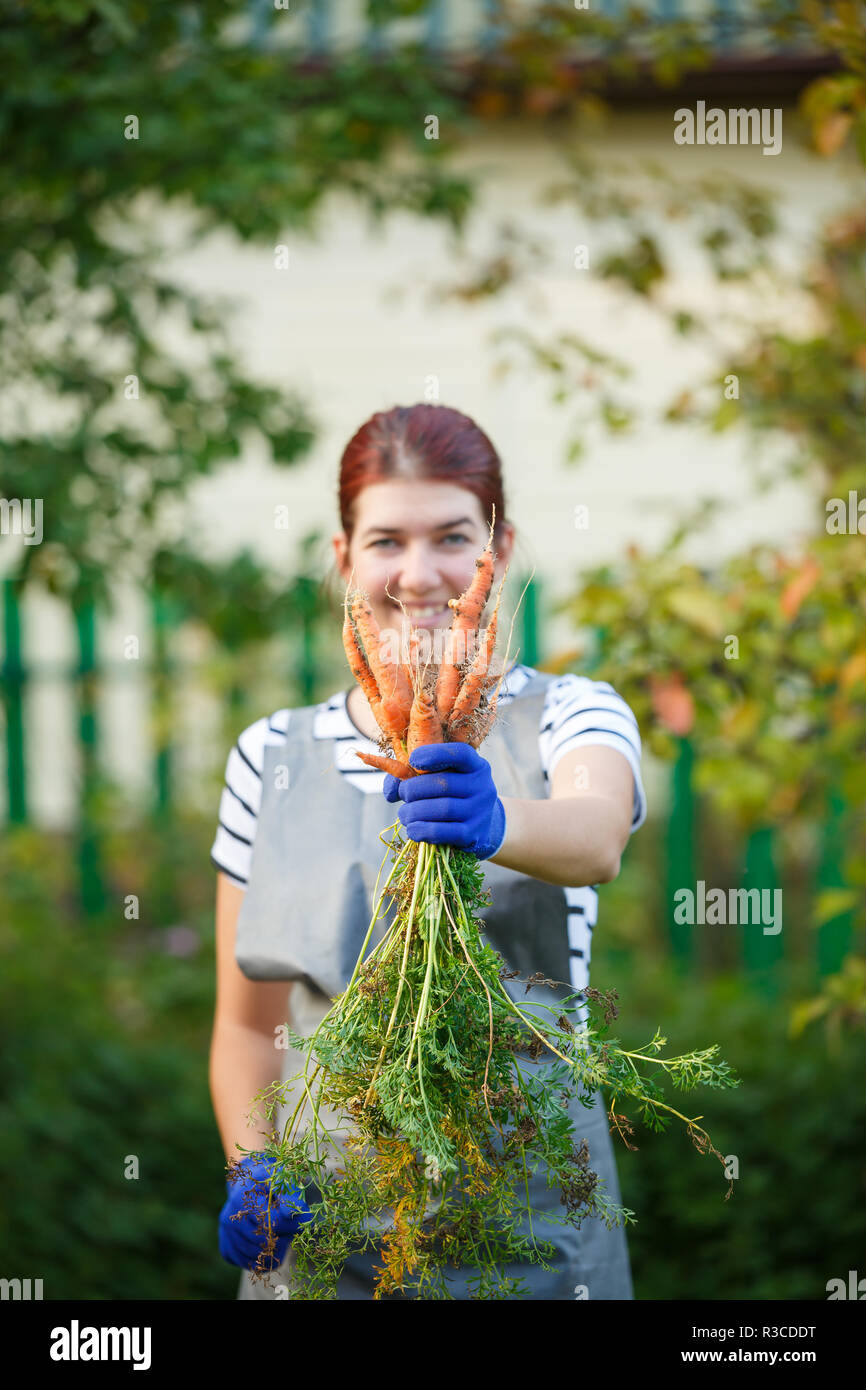 Photo of happy woman with carrot in hands on garden, blurred background ...